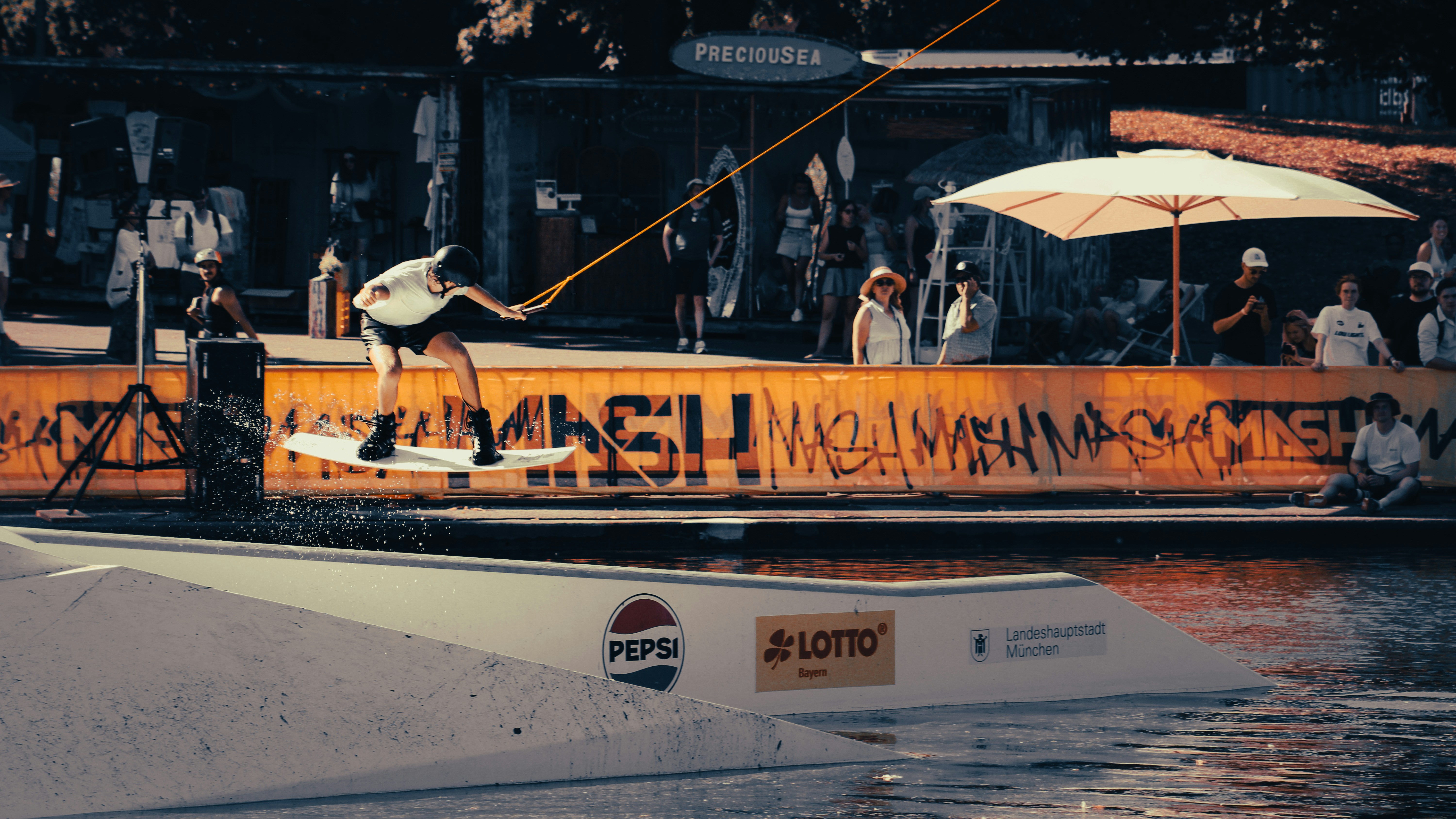 Wakeboarder in a graffiti-ed canal arena under a bright parasol