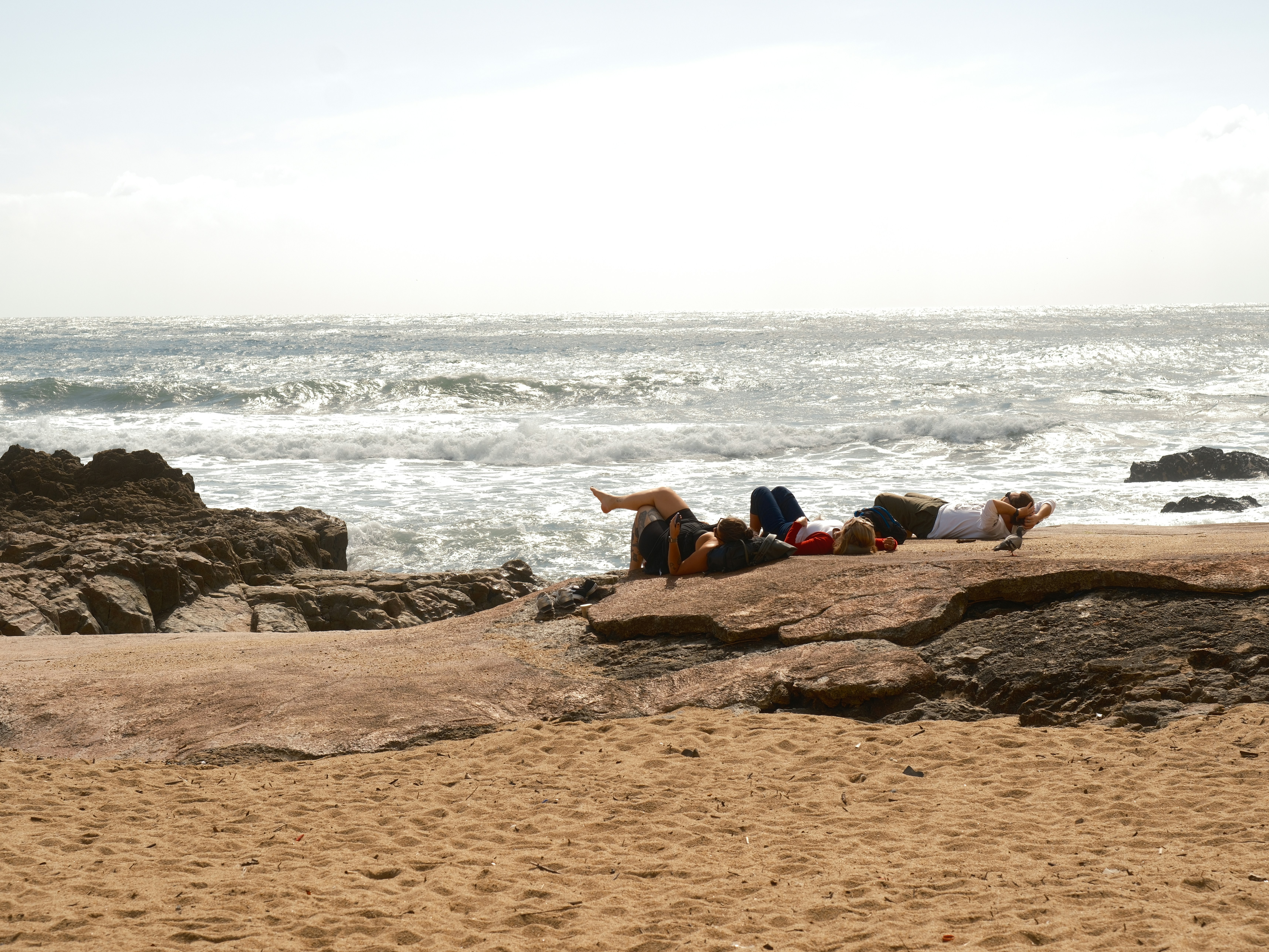 Sunlit Beachhum: People Repose on Rock Formations by the Sea