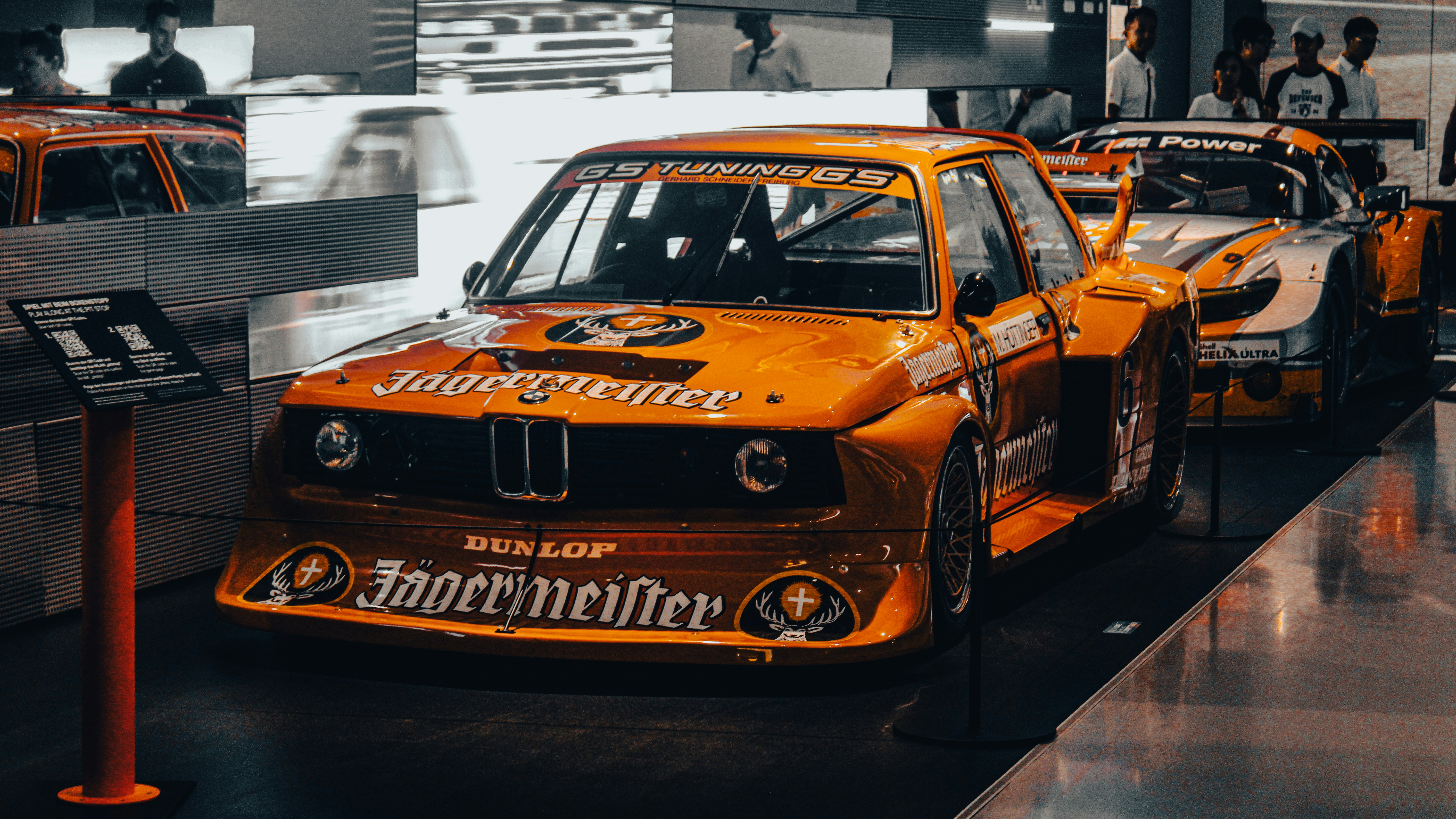 Orange race car lineup: vintage Jägermeister livery under showroom lights