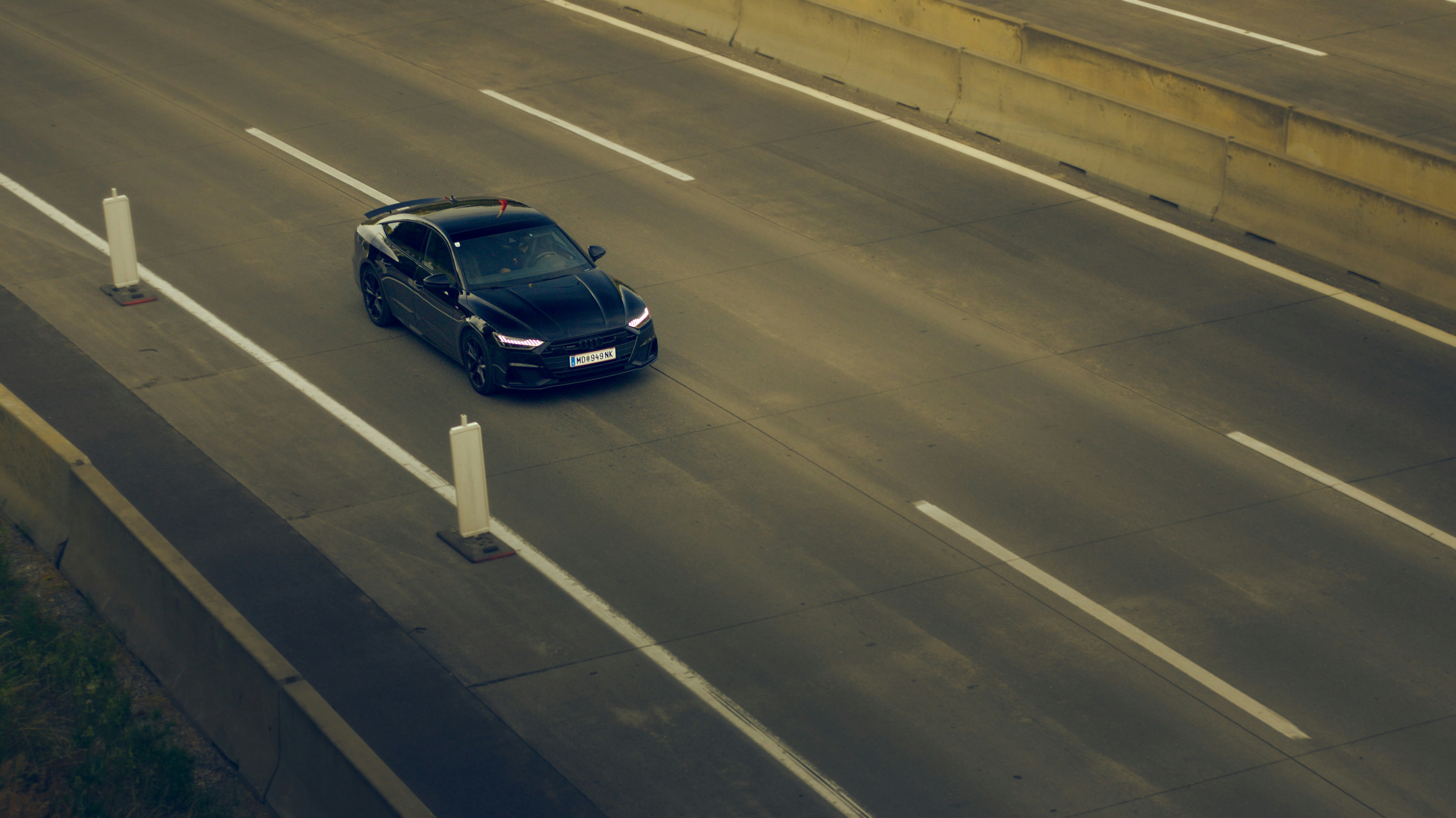 A solitary black sedan cruises a sunlit freeway