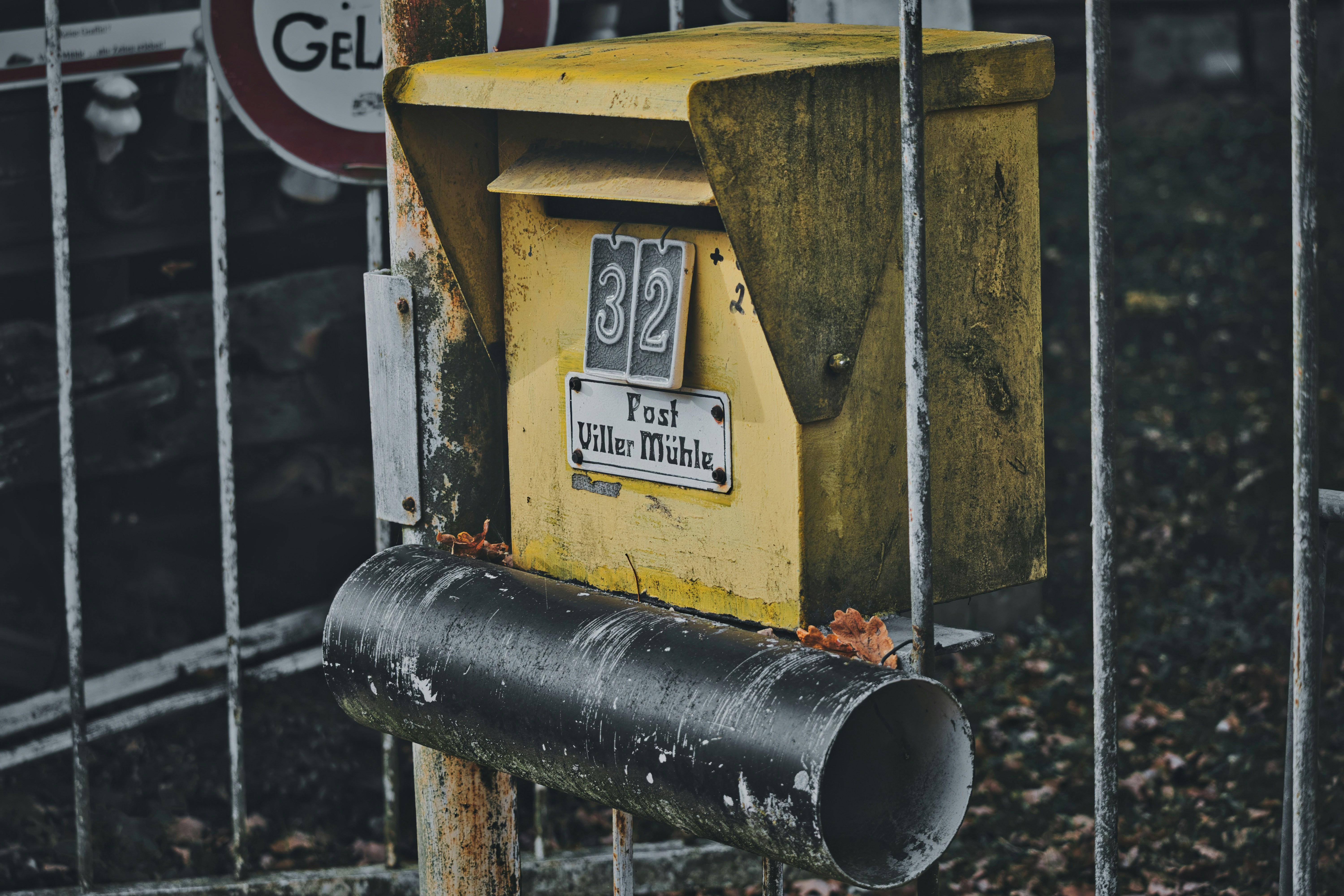 Weathered yellow mailbox with blocking bars and a curved mail chute