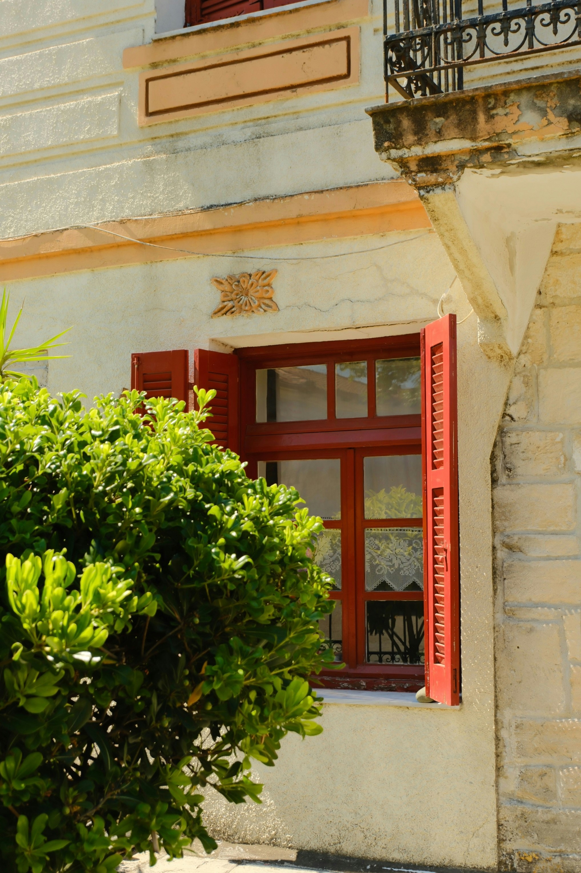 Red shutters on a building with green foliage.