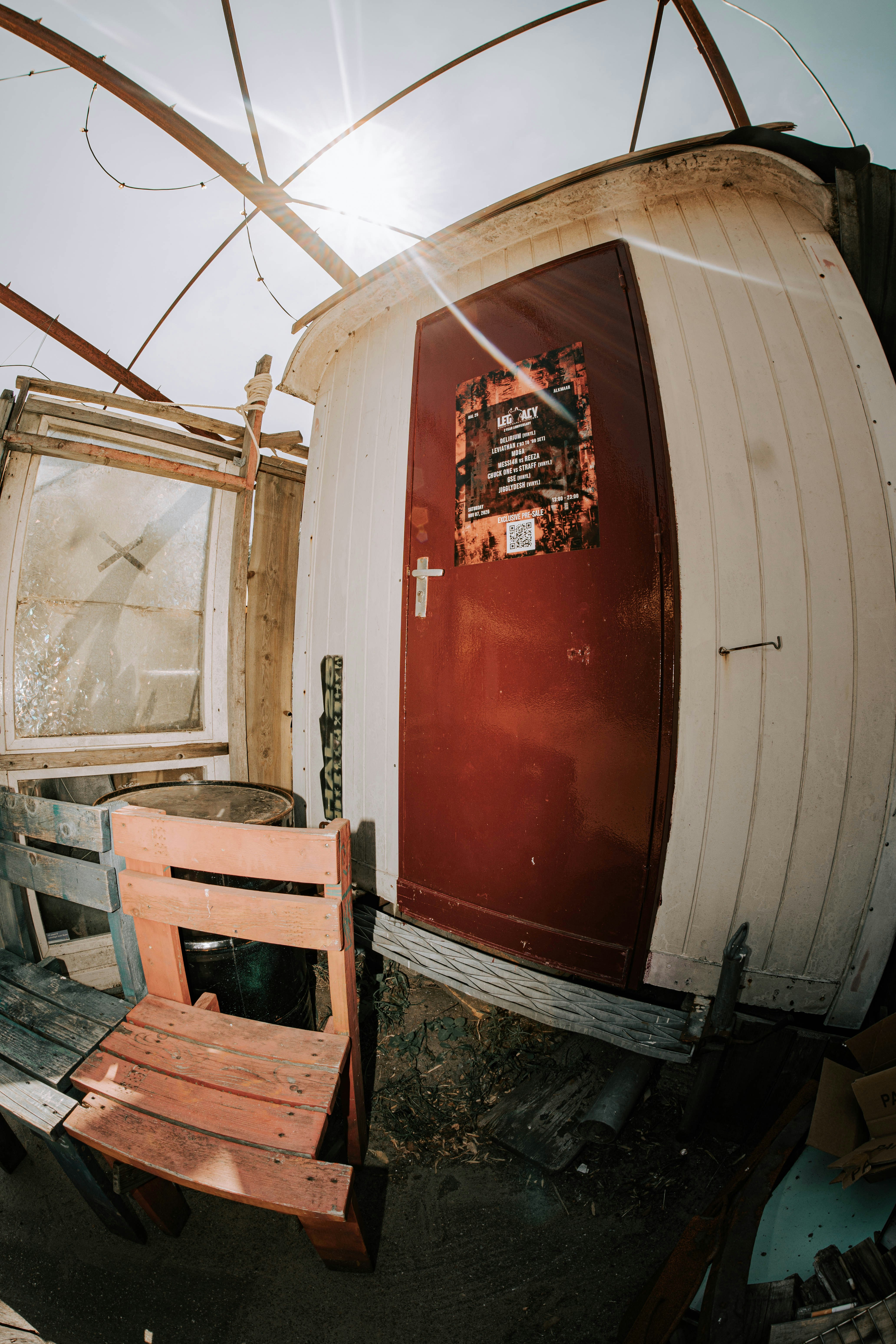 Sunlit doorway of a weathered shed framed by curved glass and string lights