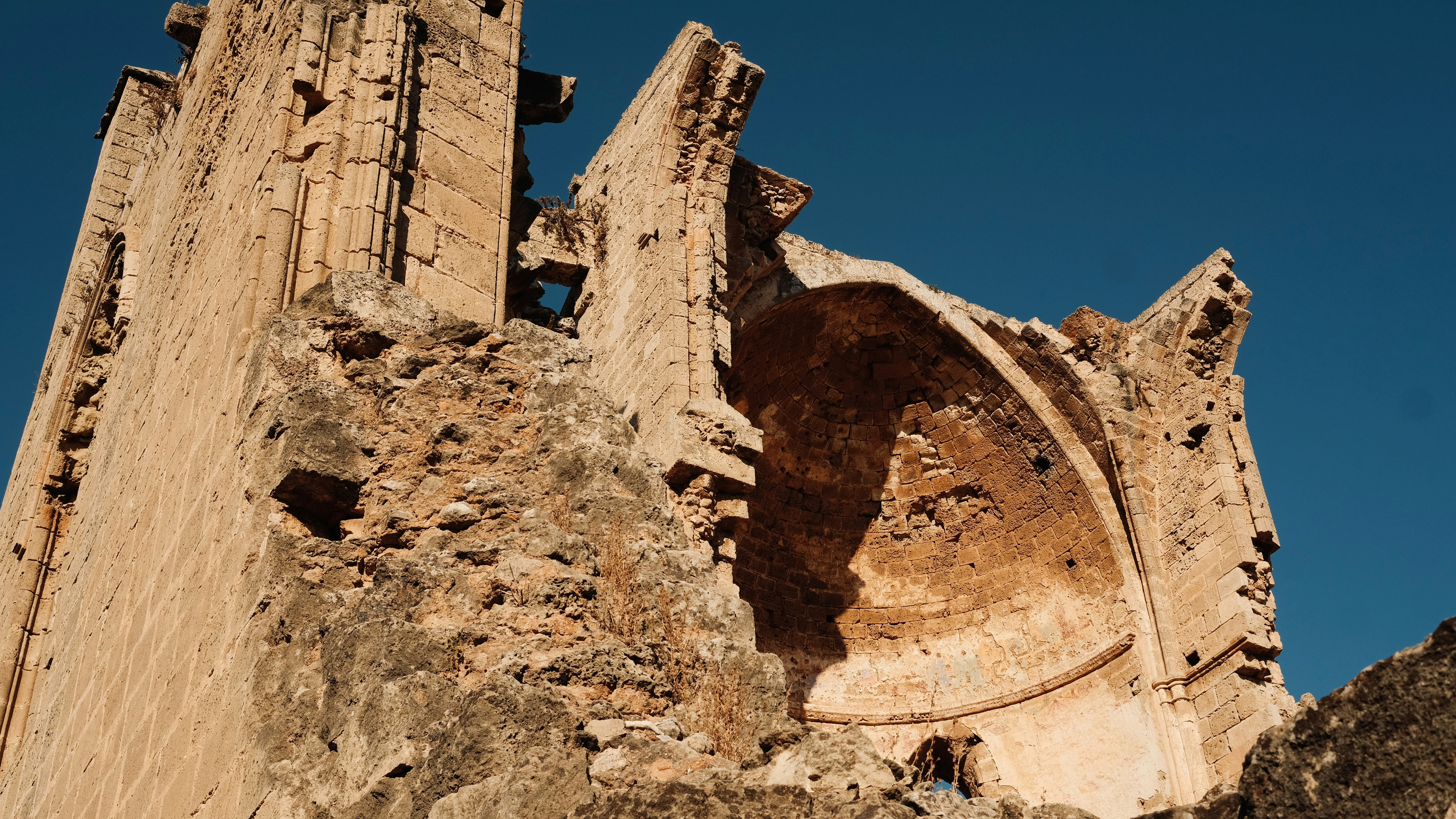 Weathered stone ruins of a cathedral rise against a crisp blue sky, with arches and crumbling walls telling a tale of time and neglect.