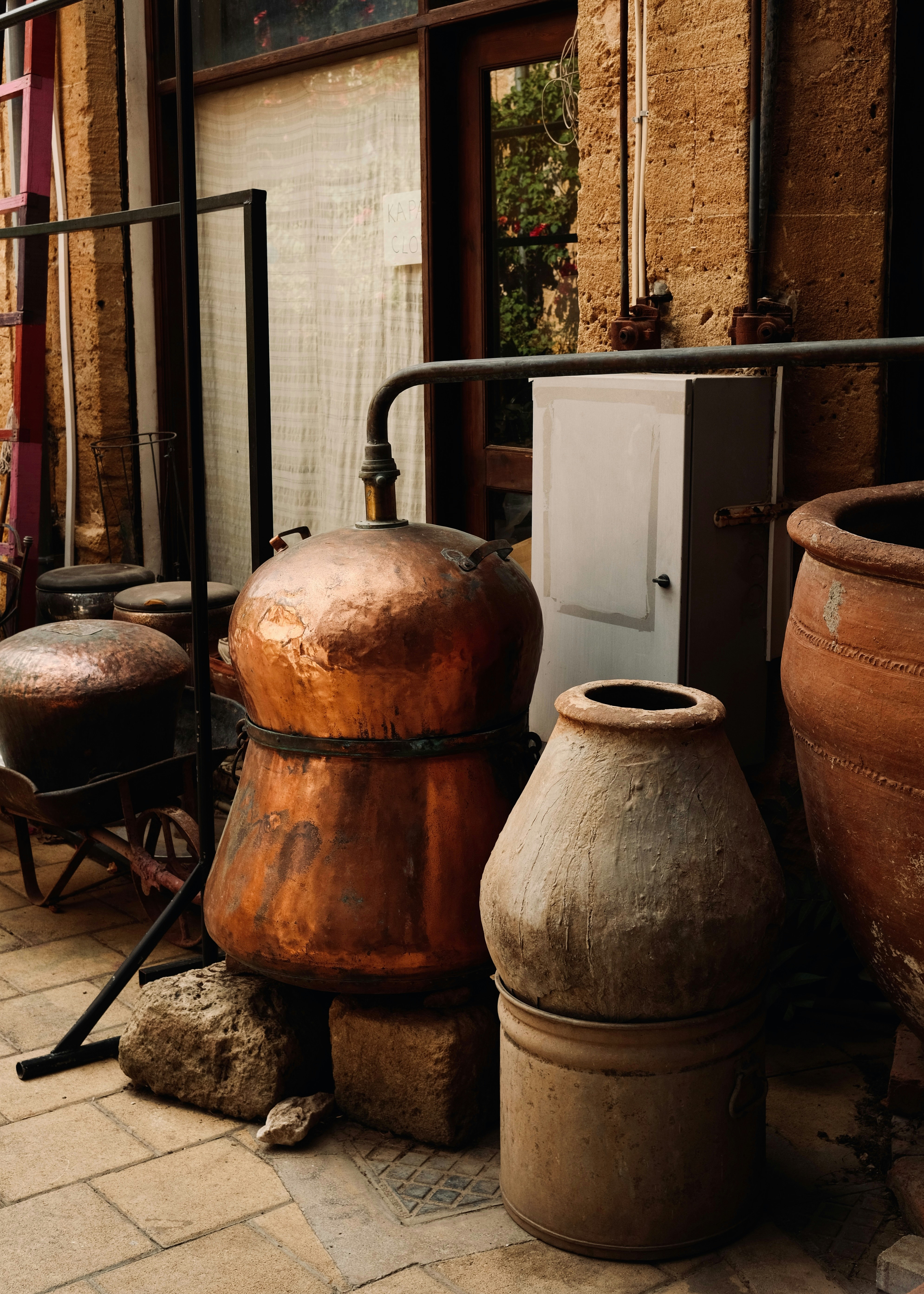 Old copper still and traditional clay pots outdoors.
