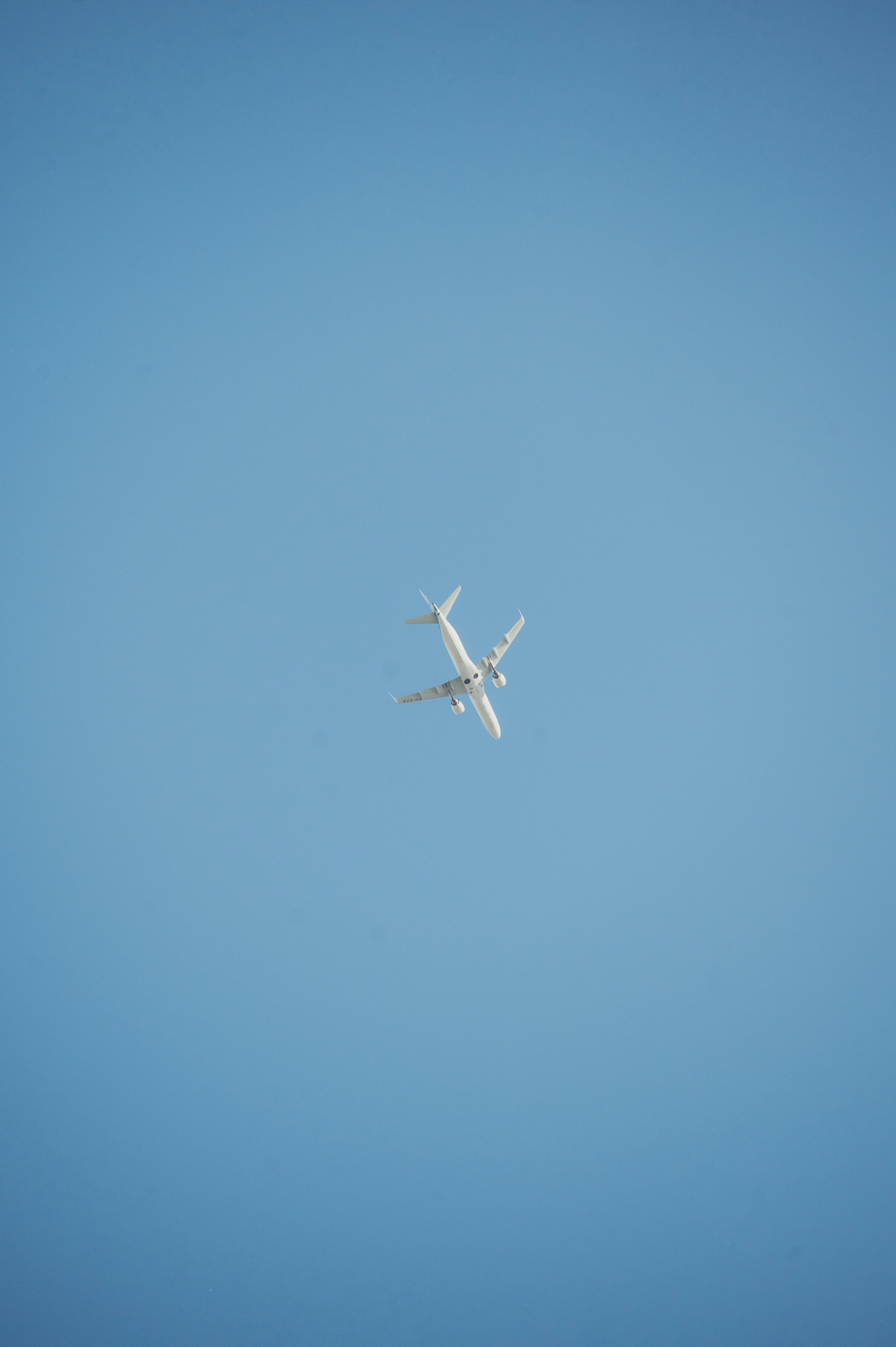 White jet soars through a blue sky, centered with ample negative space surrounding the aircraft. A minimalist capture emphasizing separation from the horizon and sense of flight.