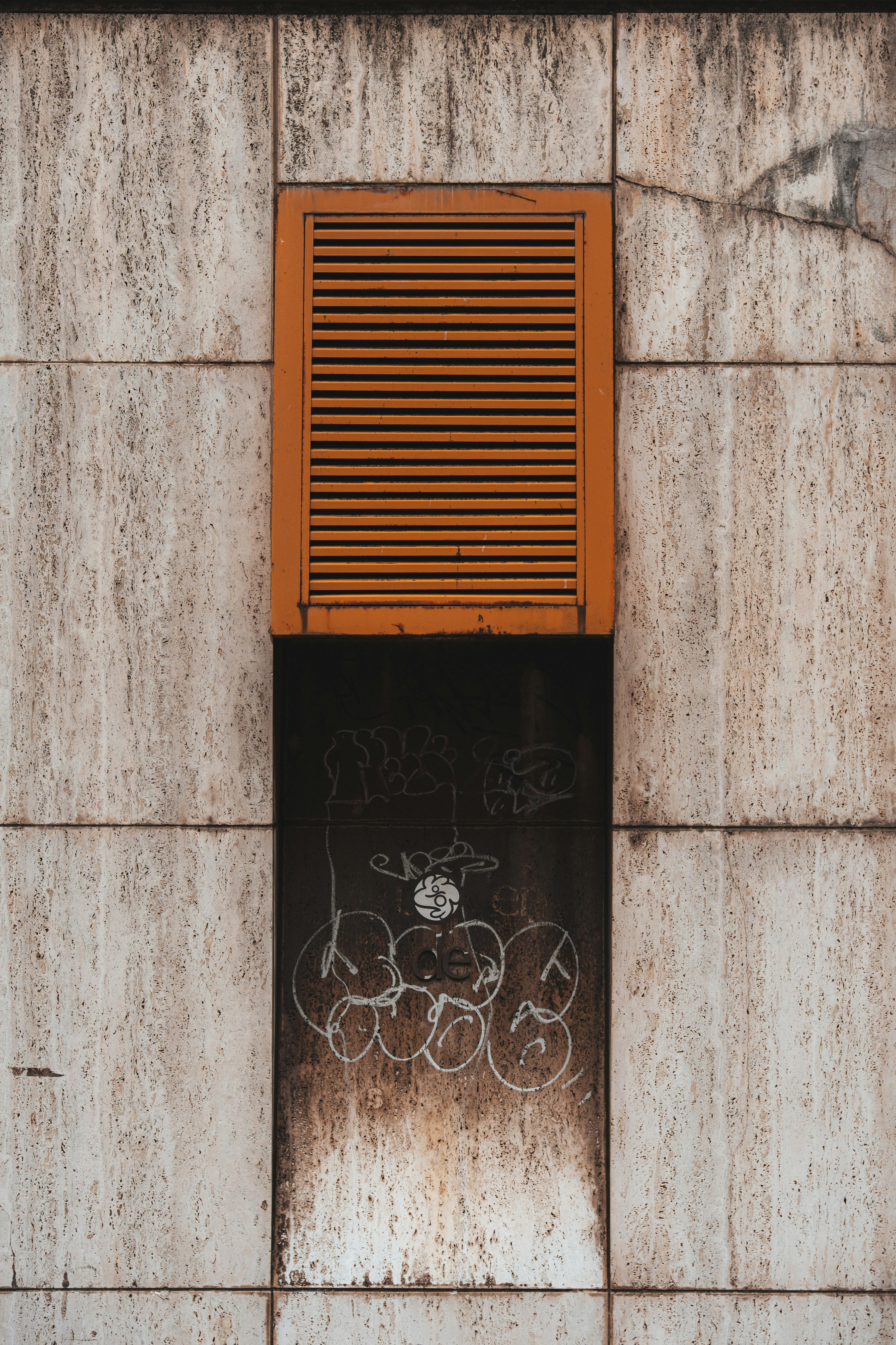 Rusty vent over a graffiti-soaked recess on a weathered concrete wall