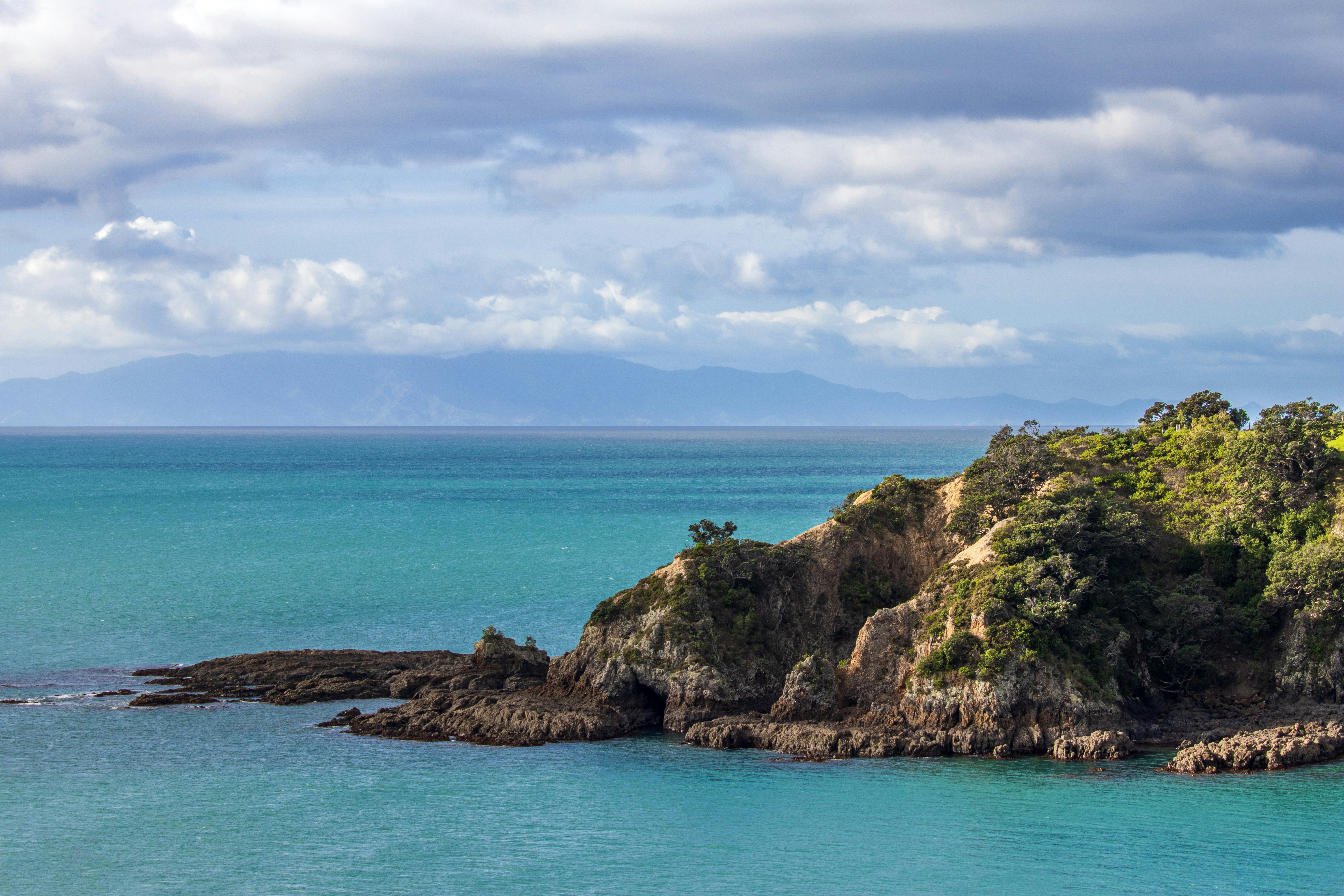 Stretch of turquoise sea meeting rocky coastline under partly cloudy sky