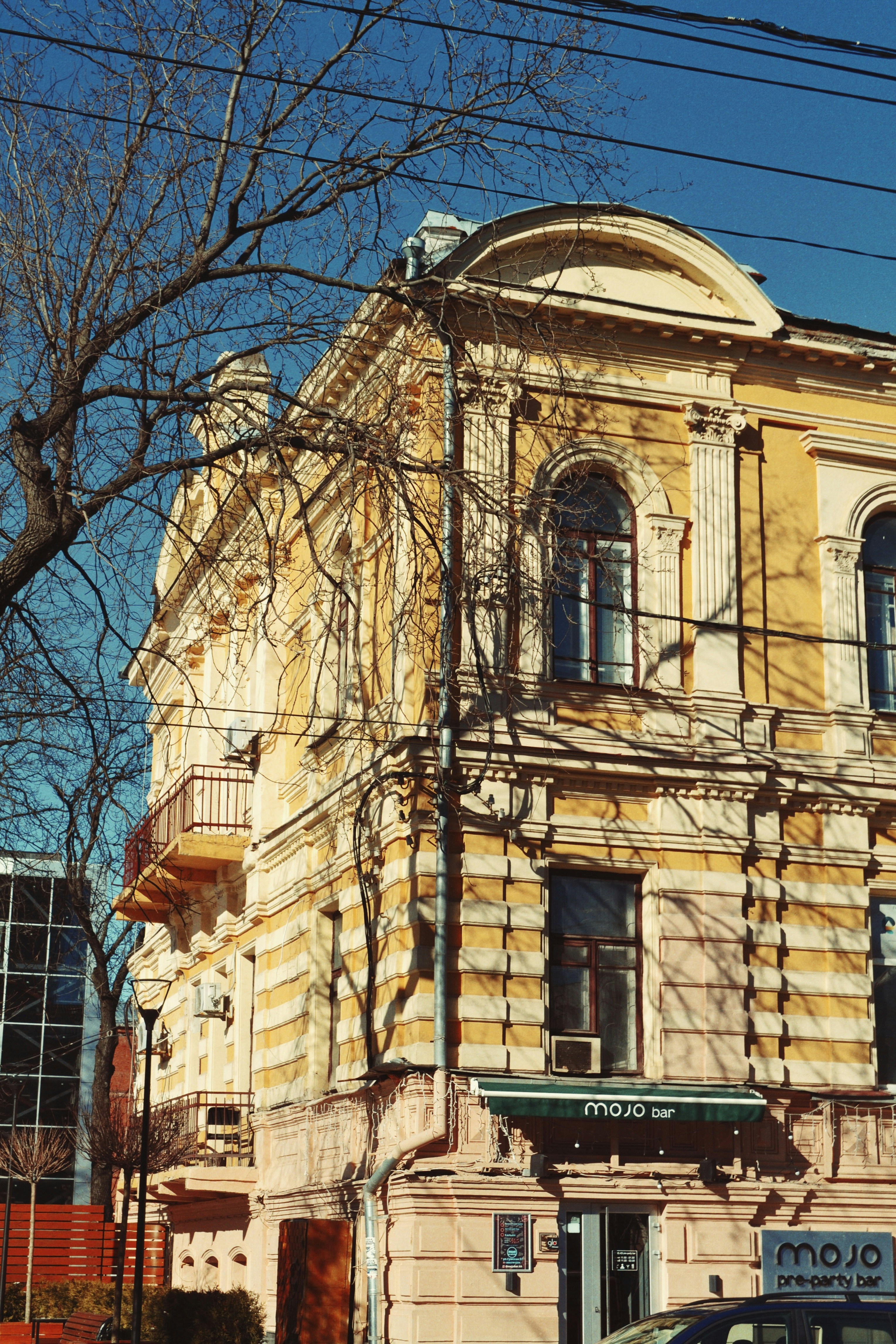 Sunlit corner of a historic yellow facade with ornate detailing and a MOJO bar sign