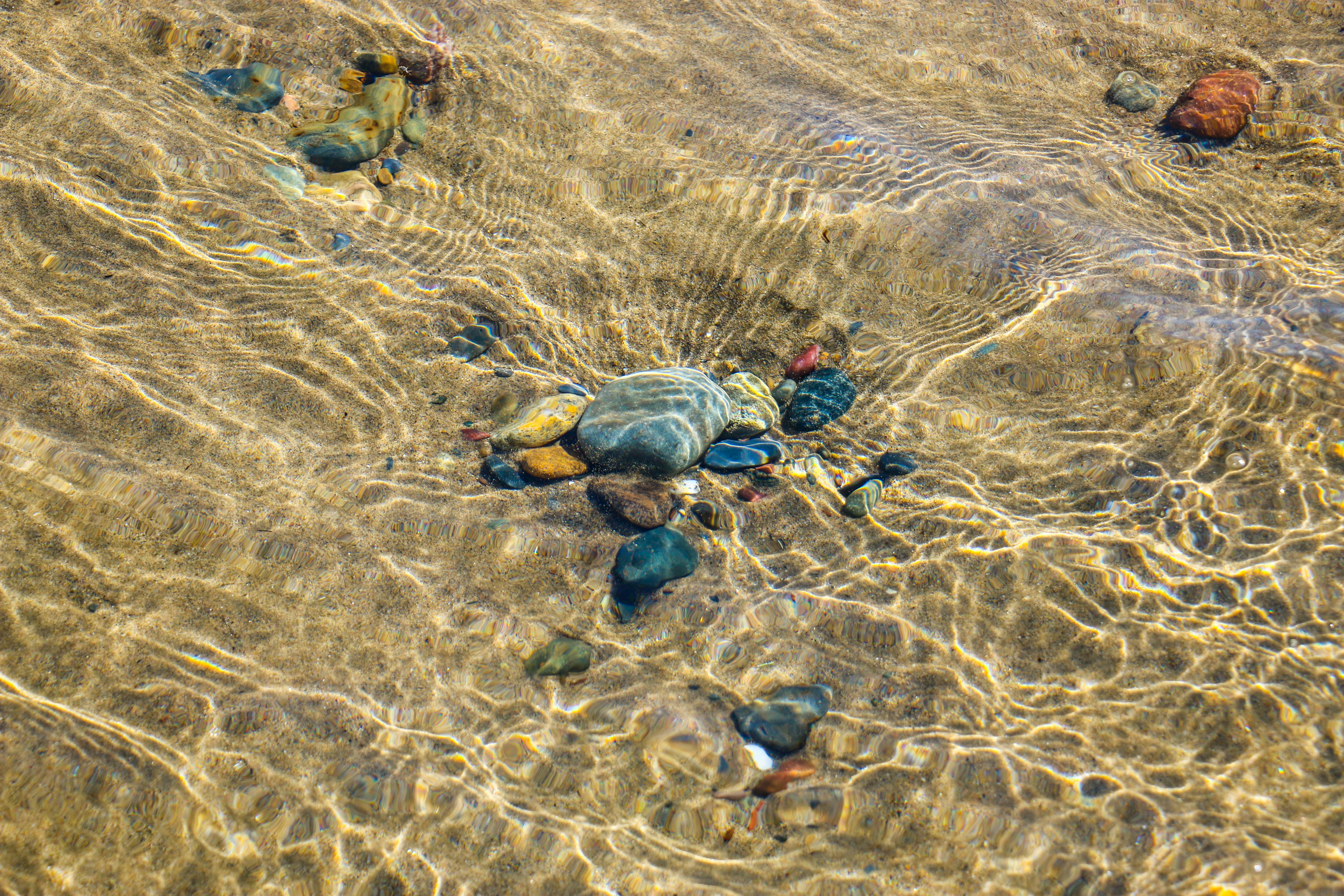 Pebble Mosaic in Sunlit Tide: Rays on the Shallow Seabed