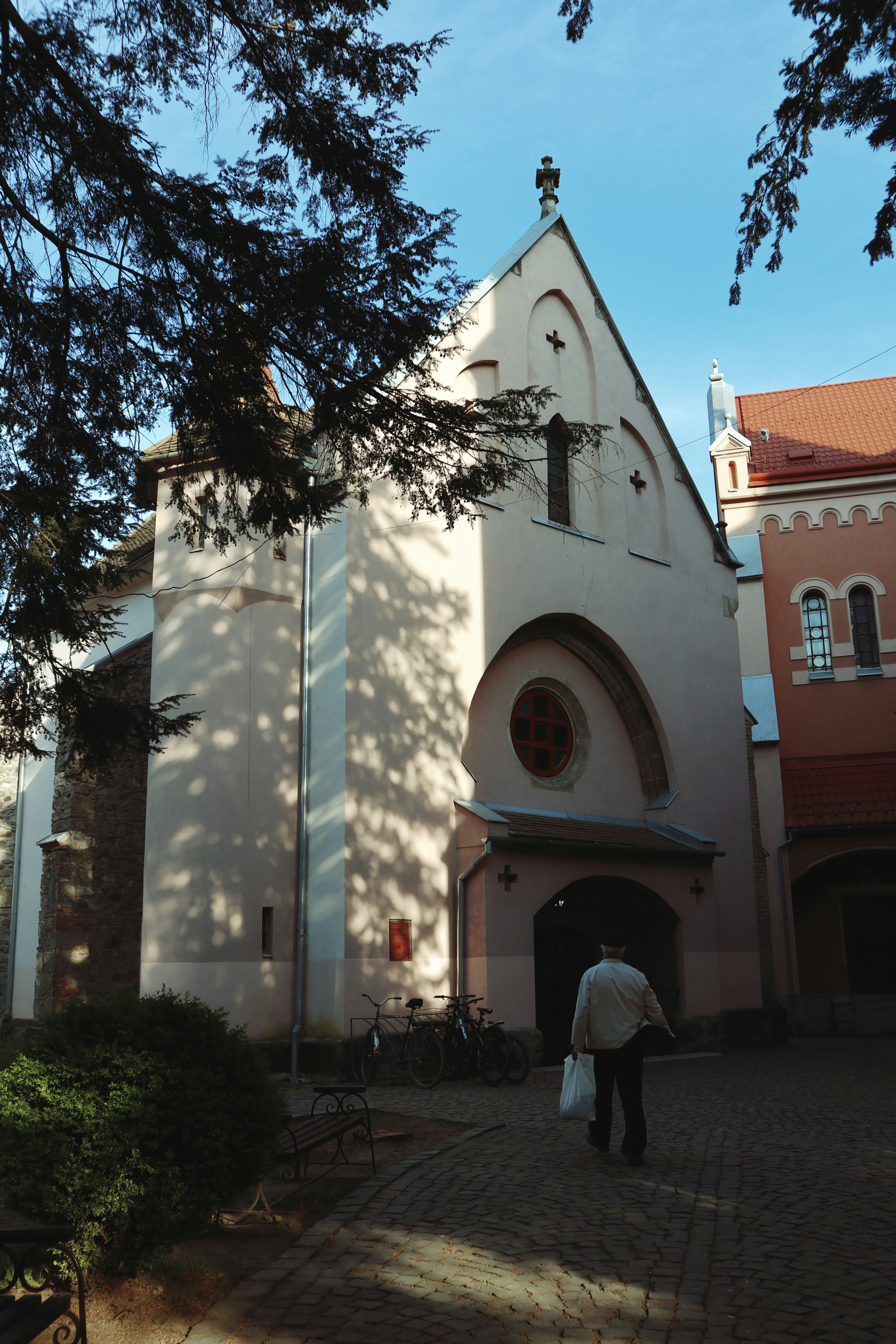 Sunlit Facade and Quiet Courtyard: A Visitor with Shopping Bag Passes Beneath a Historic Church