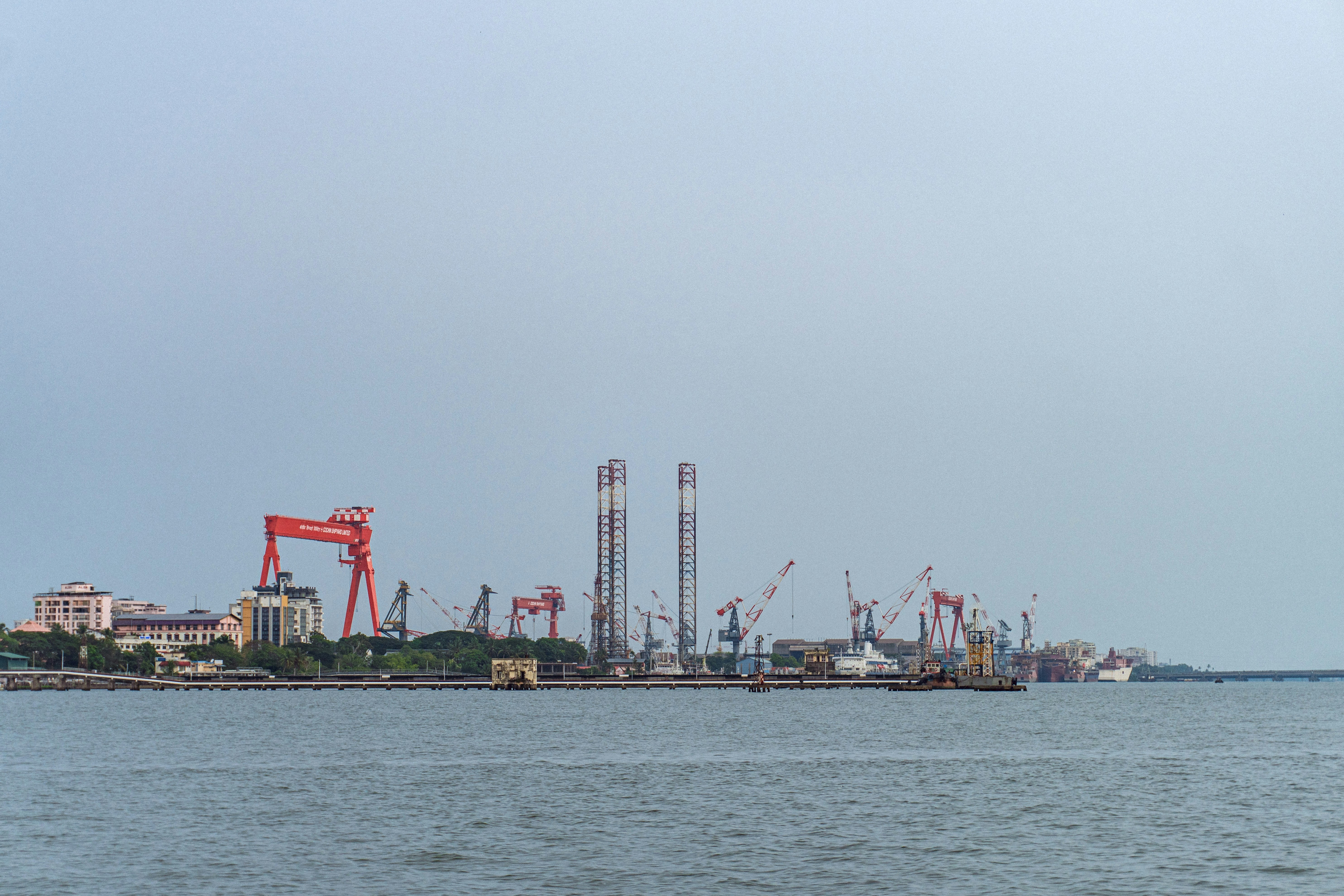 Coastal Construction Horizon: Red Cranes and Silhouettes Along the Breakwater