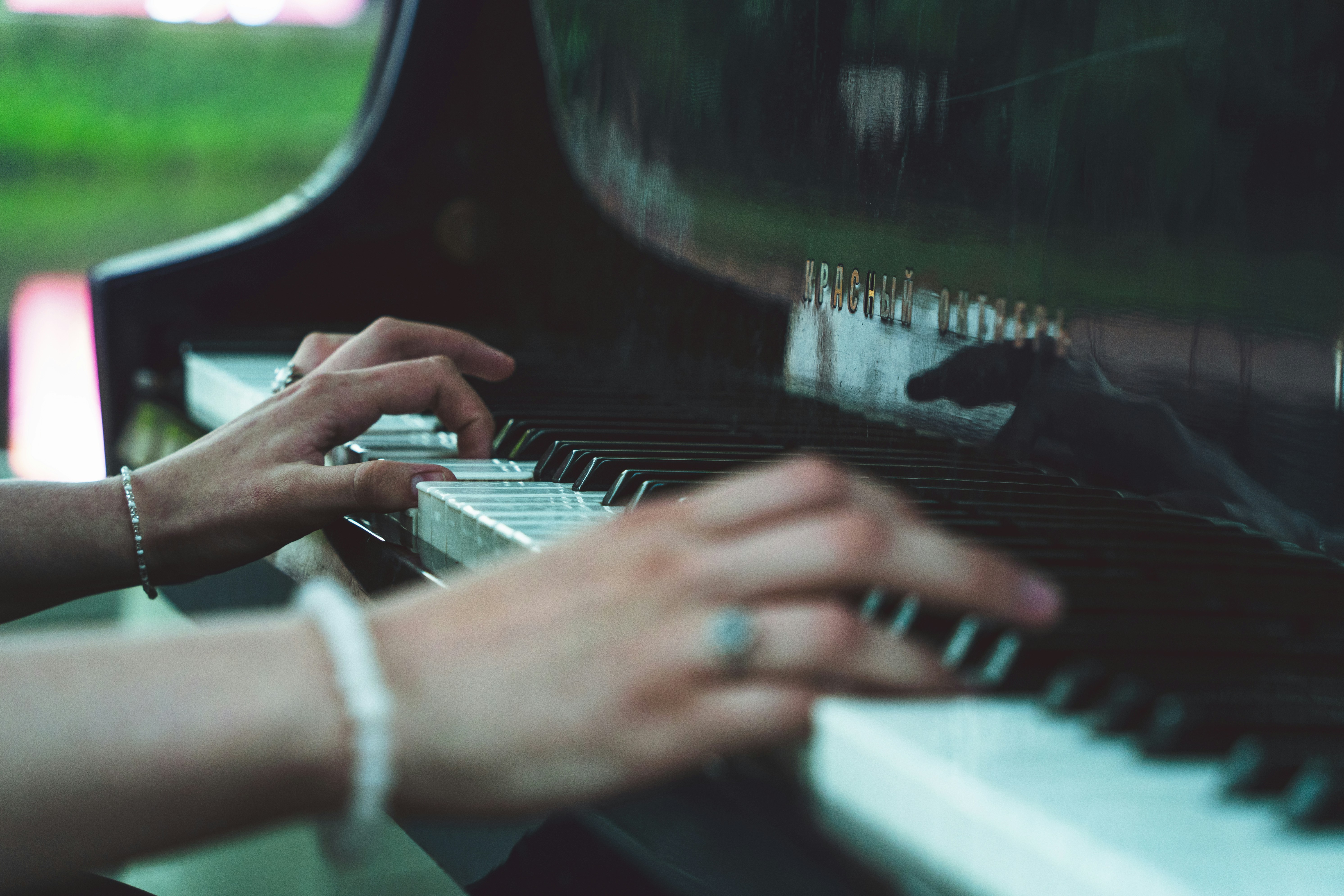Hands playing the keys of a black piano outdoors.