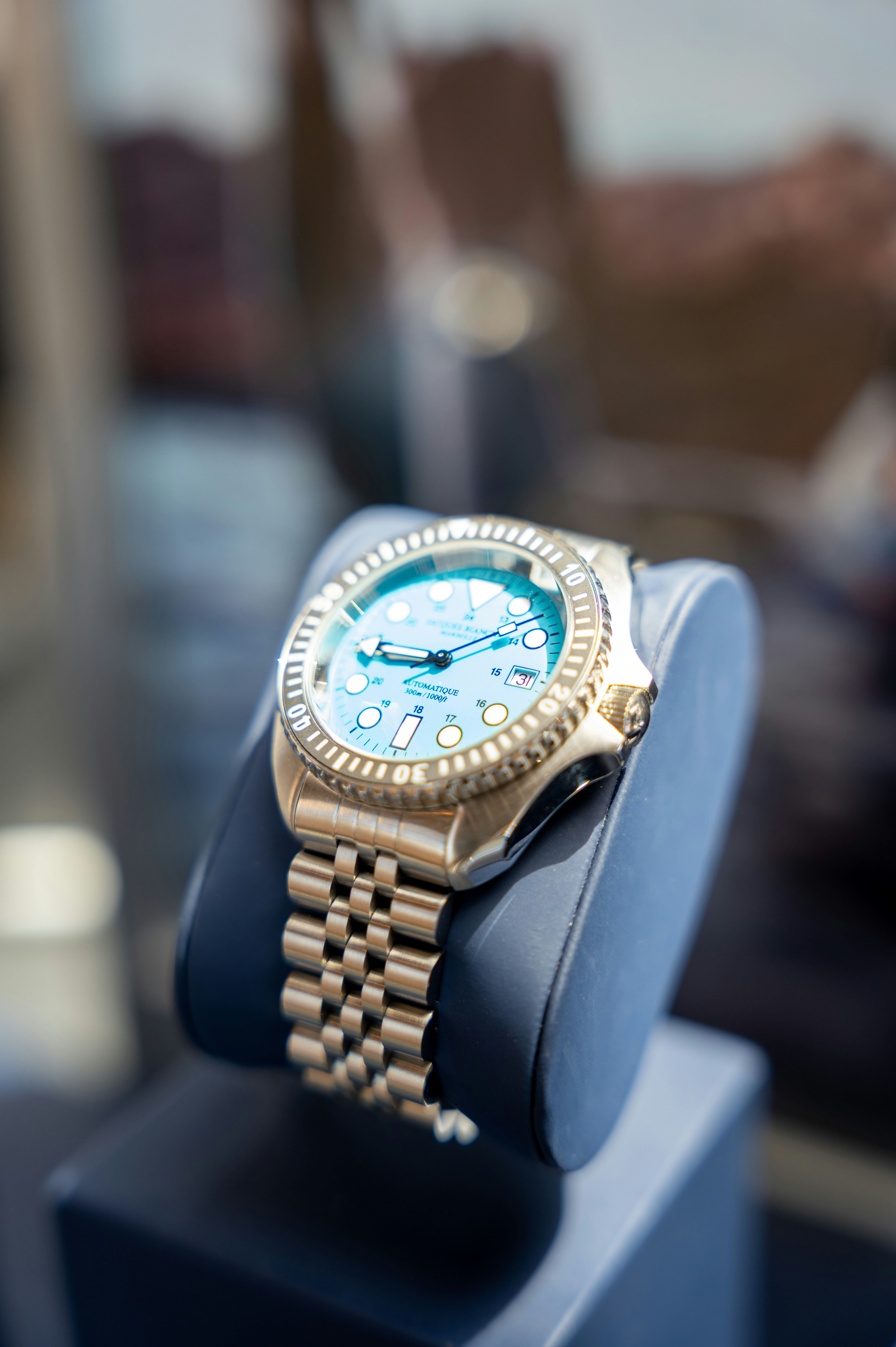 Shiny luxury dive watch on a cushioned display, foreground-focused with a blurred storefront backdrop.