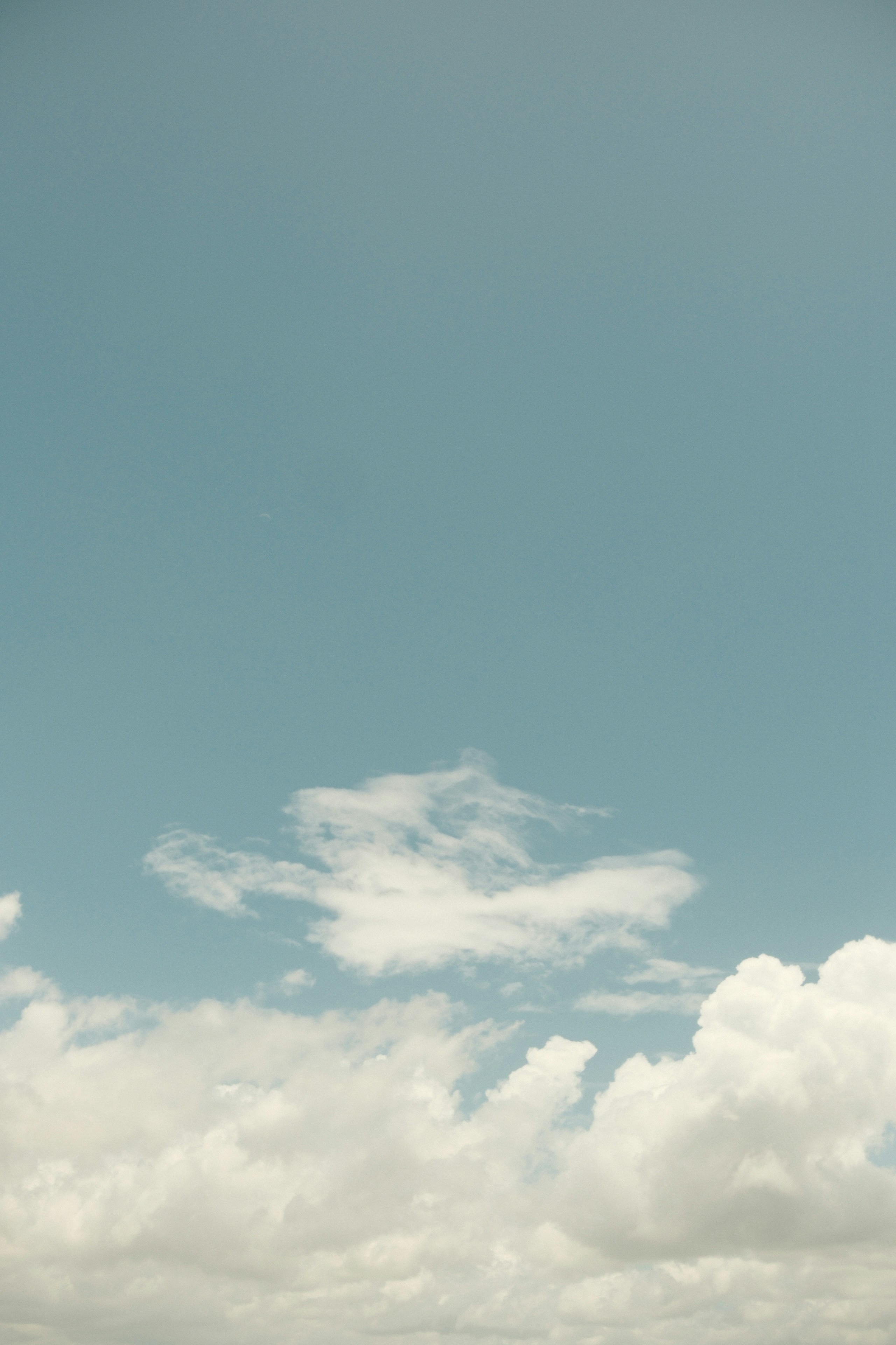 A vast blue sky with scattered white clouds occupying the lower portion, emphasizing open space. This is a plain sky scene with no foreground subjects, suitable as a background or stock atmosphere.