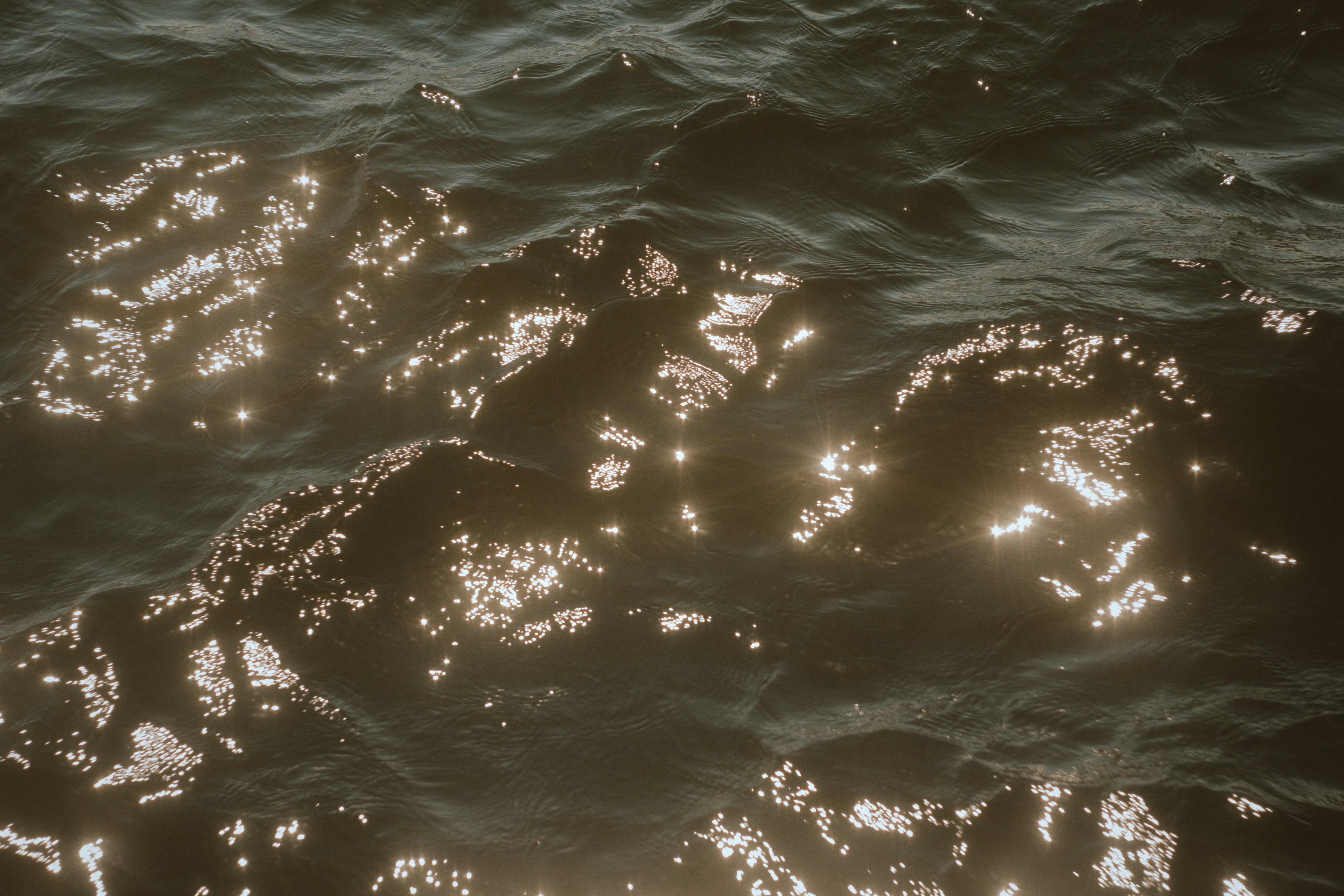 A cinematic, minimalist shot of golden sun glints sparkling on the dark, textured ripples of the Suez Canal in Port Said, Egypt. The high-contrast reflections create a serene and abstract maritime atmosphere.