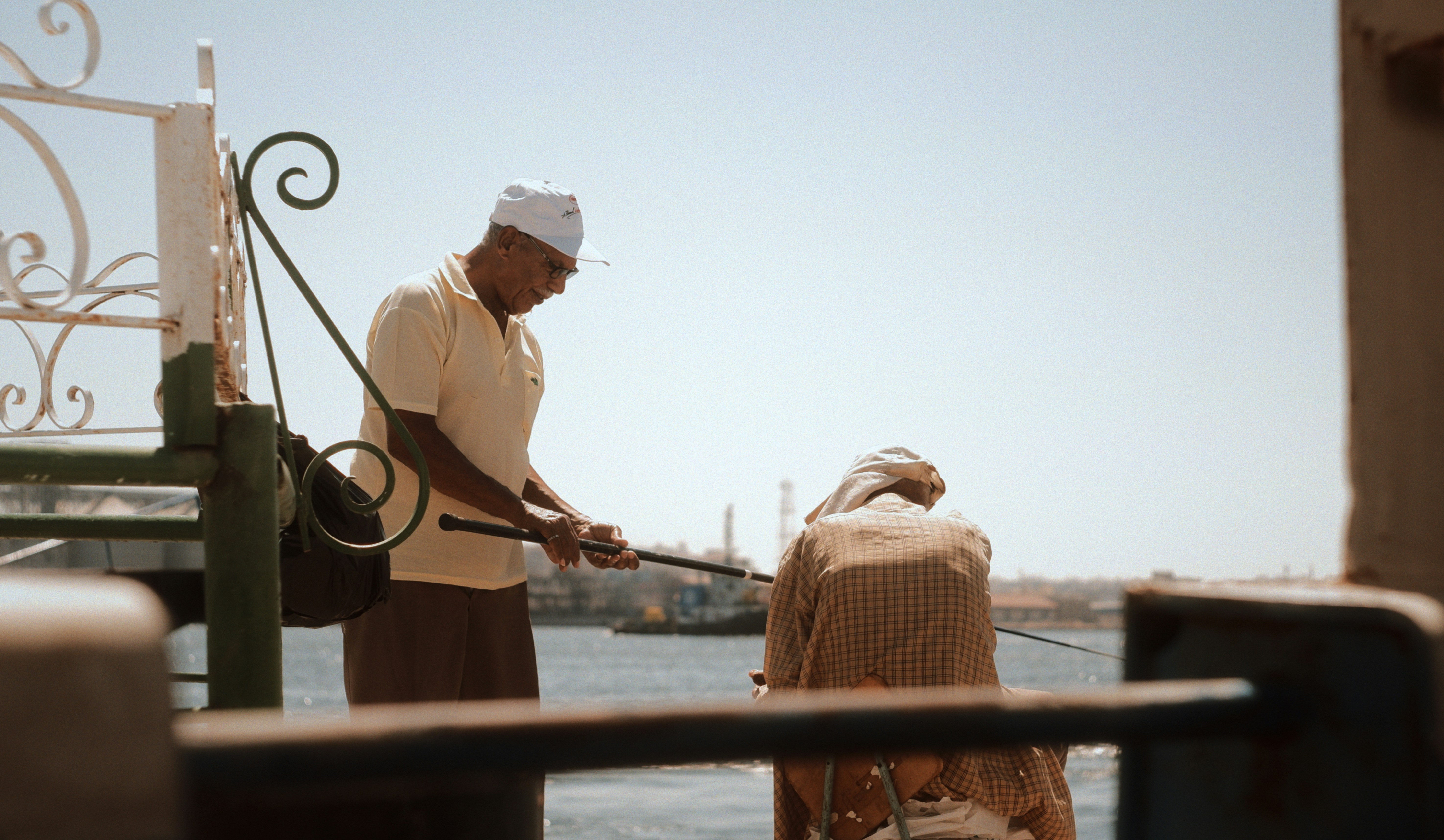 An intimate photo series from Port Said, Egypt, focusing on the lives of local fishermen at the entrance of the Suez Canal. Shot on a Fujifilm X-A5, the collection opens with a detailed close-up of a fisherman's weathered hands mending his net, setting a tone of traditional labor and skill. It features candid, documentary-style portraits of fishermen working and relaxing along the canal banks, framed by the unique blend of historic architecture and massive international shipping. The entire series is rendered with a warm, grain-enhanced 'Cinematic Film Look' that gives the documentary photogra