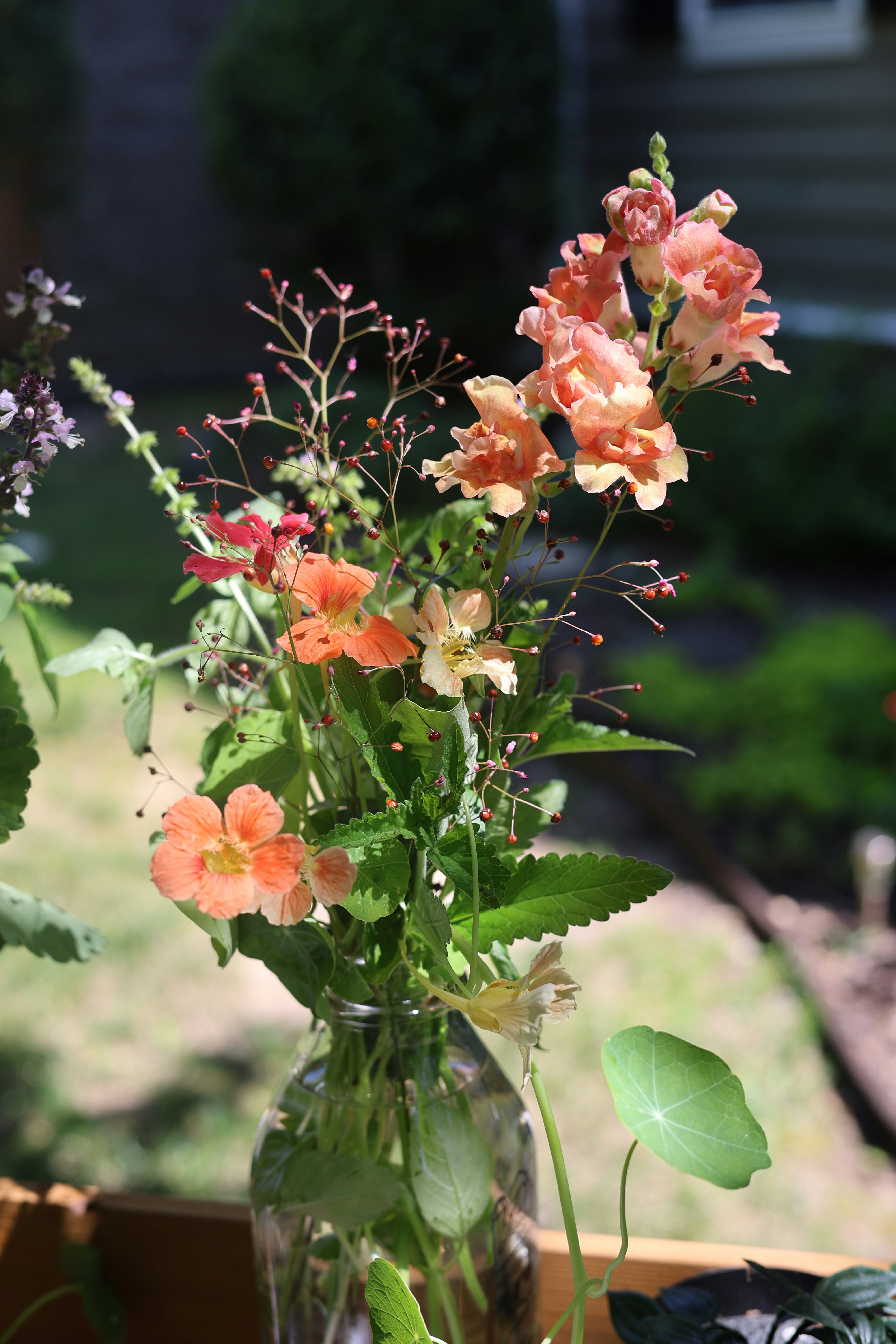 Colorful flower bouquet in a glass vase bathed in soft garden light, with a blurred outdoor background emphasizing the arrangement.
