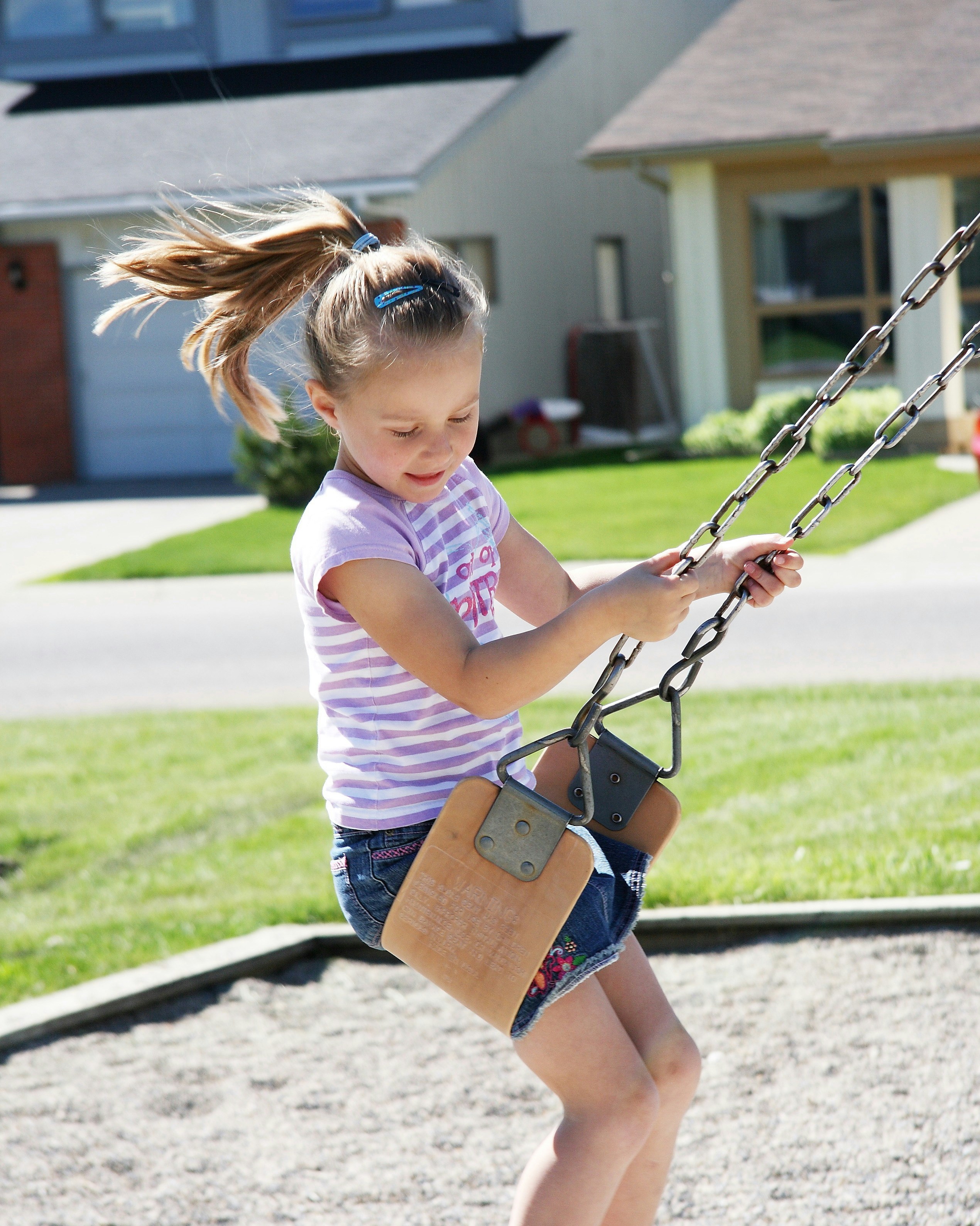 Swinging Joy: A GIRL in Striped Purple Tops and Denim Shorts Soars in a Sunlit Yard