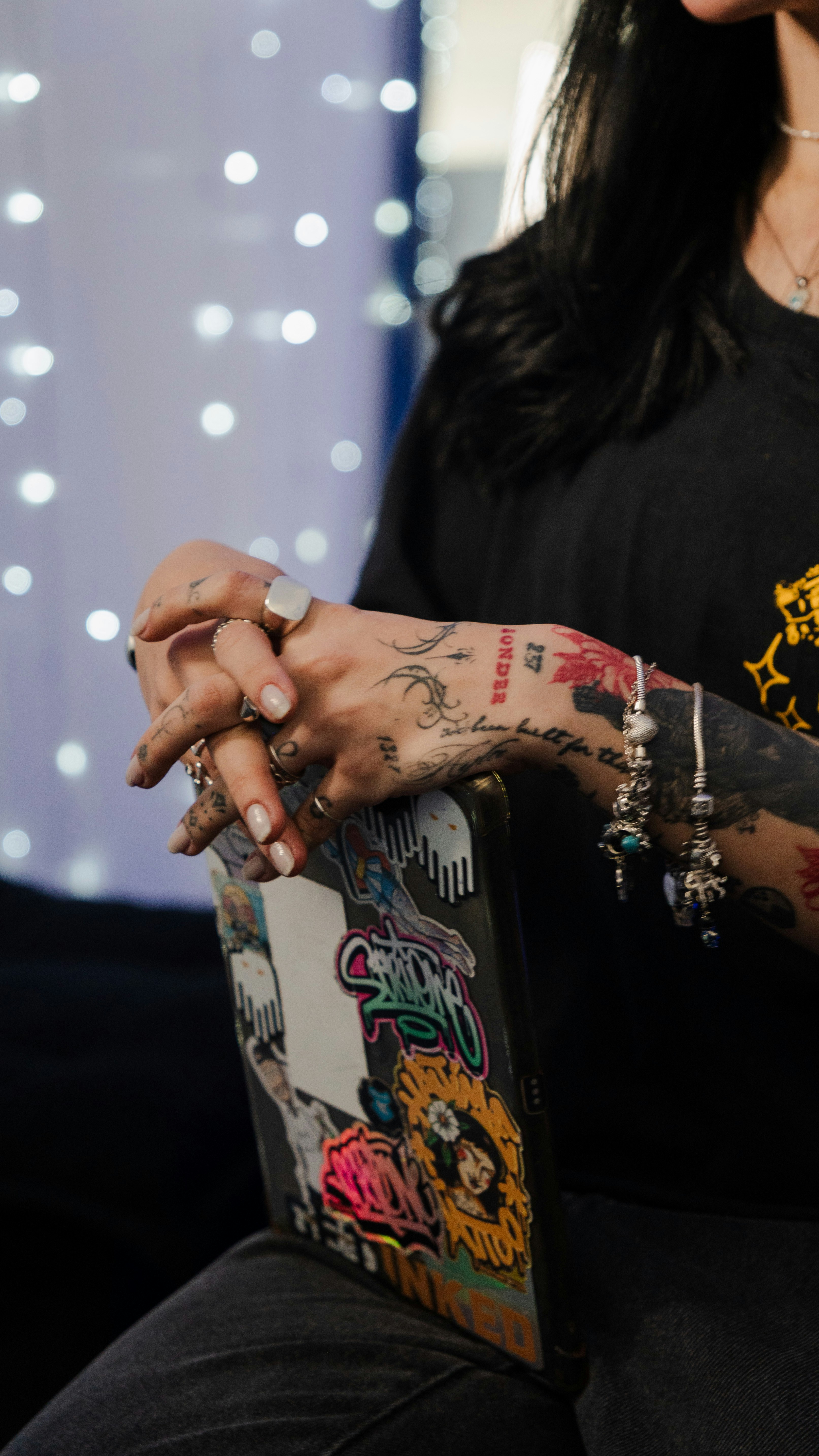 Tattooed Hands and Stickered Tablet: Quiet Confidence in a Dimly Lit Corner