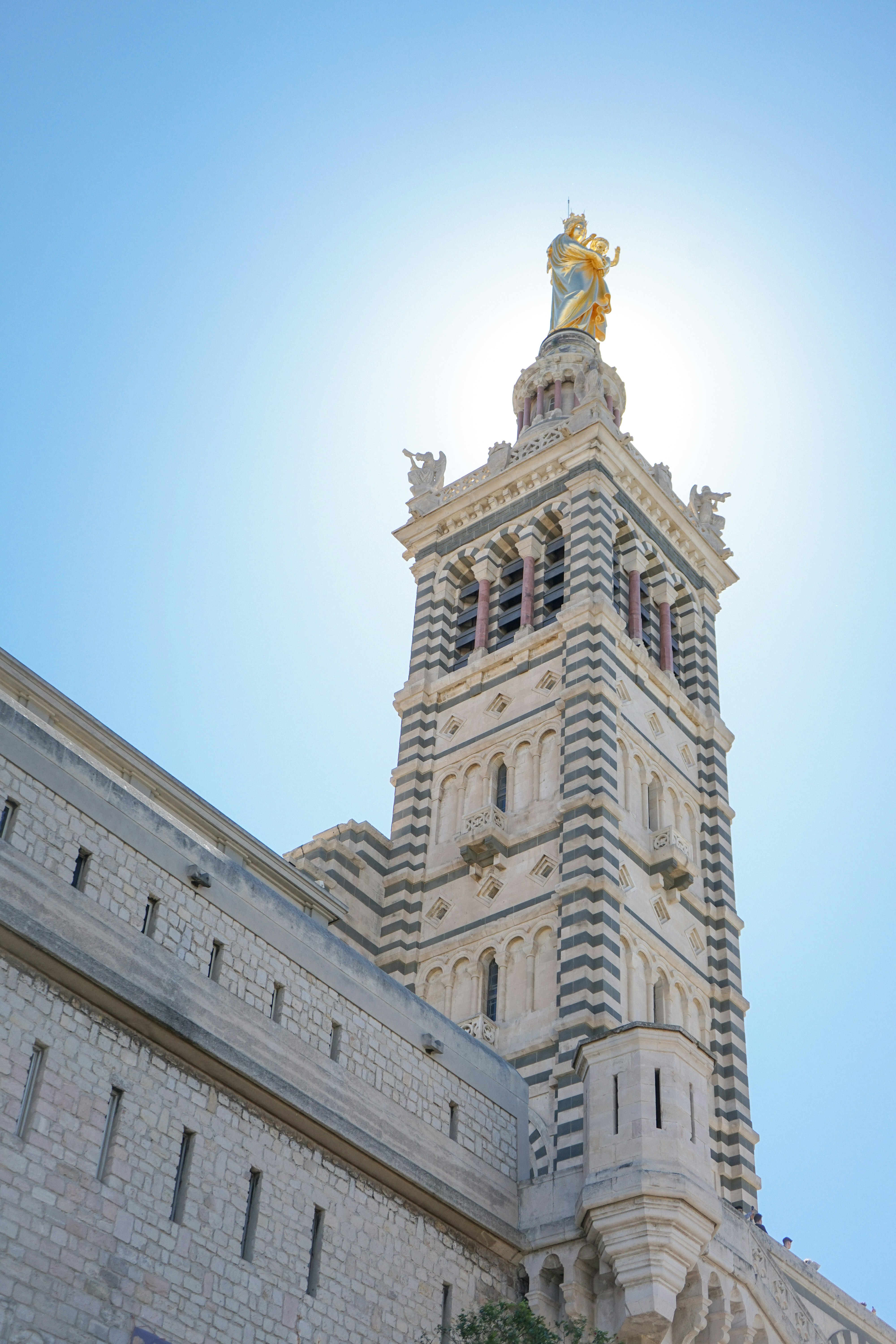 Golden Statue Above the Striped Bell Tower Rises Against a Brilliant Blue Sky