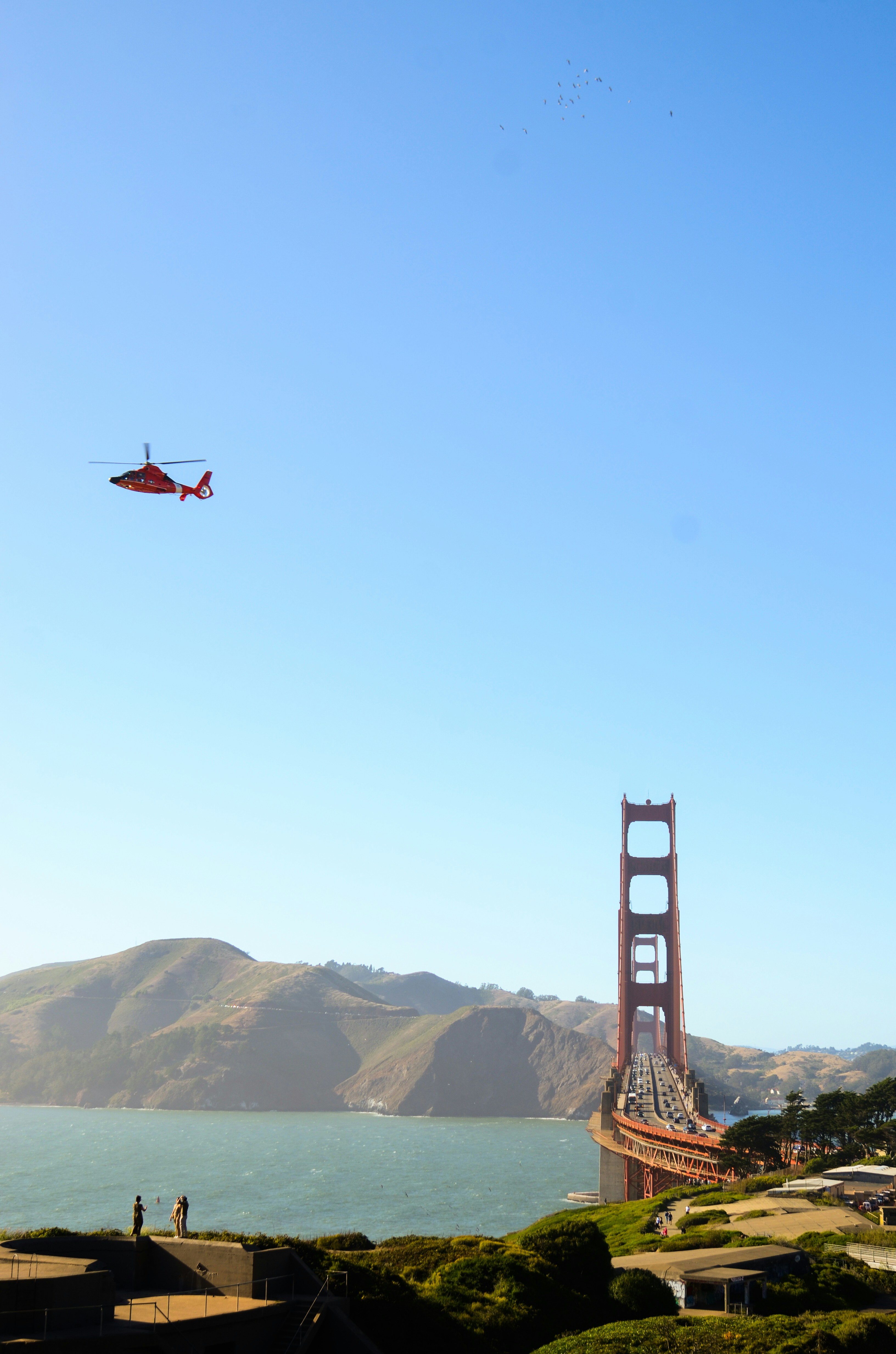 Red helicopter over the Golden Gate Bridge: airborne silhouette against a clear blue sky