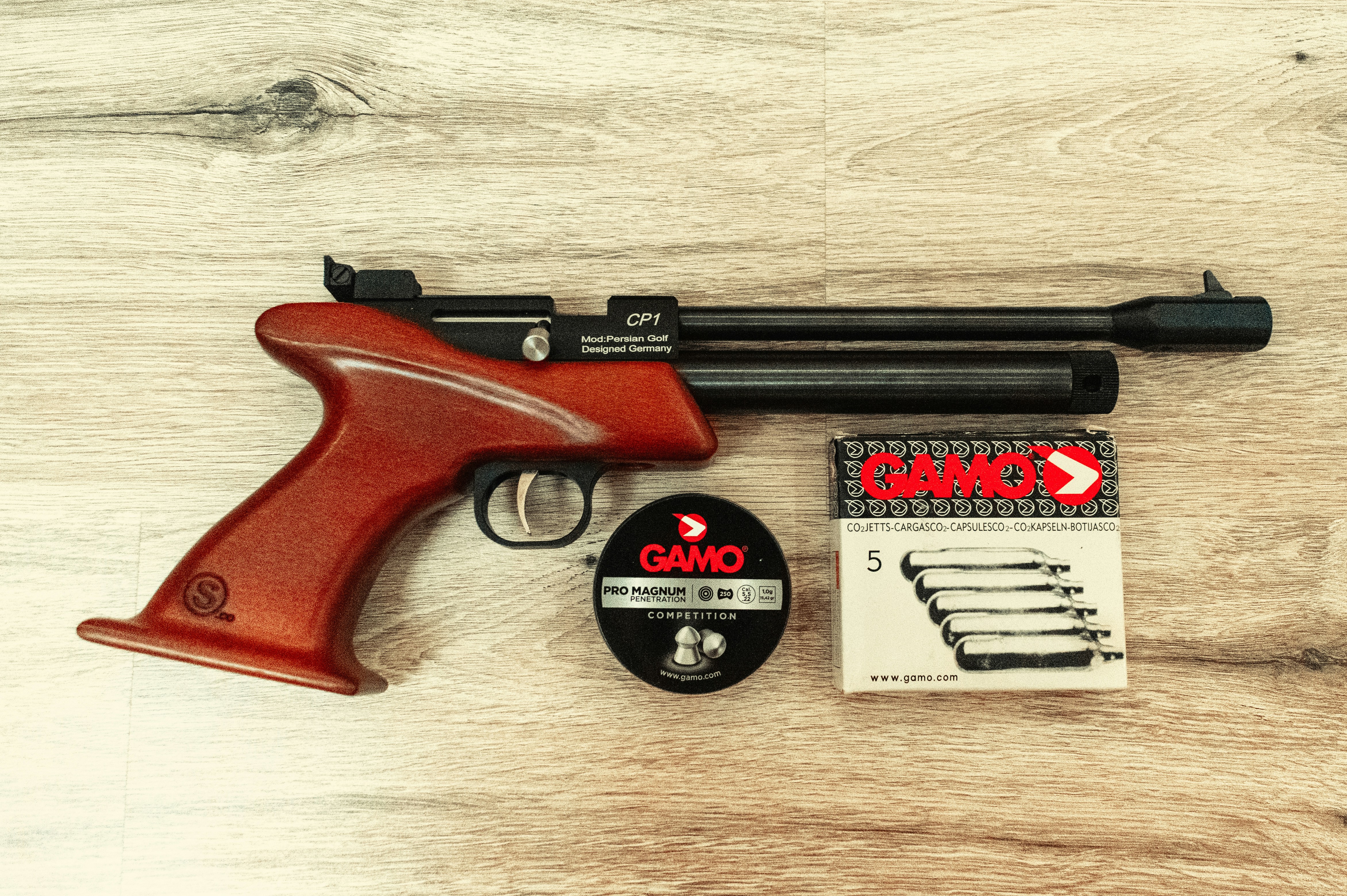Wooden-handled air pistol with CO2 cylinder and pellets laid out on light wood surface