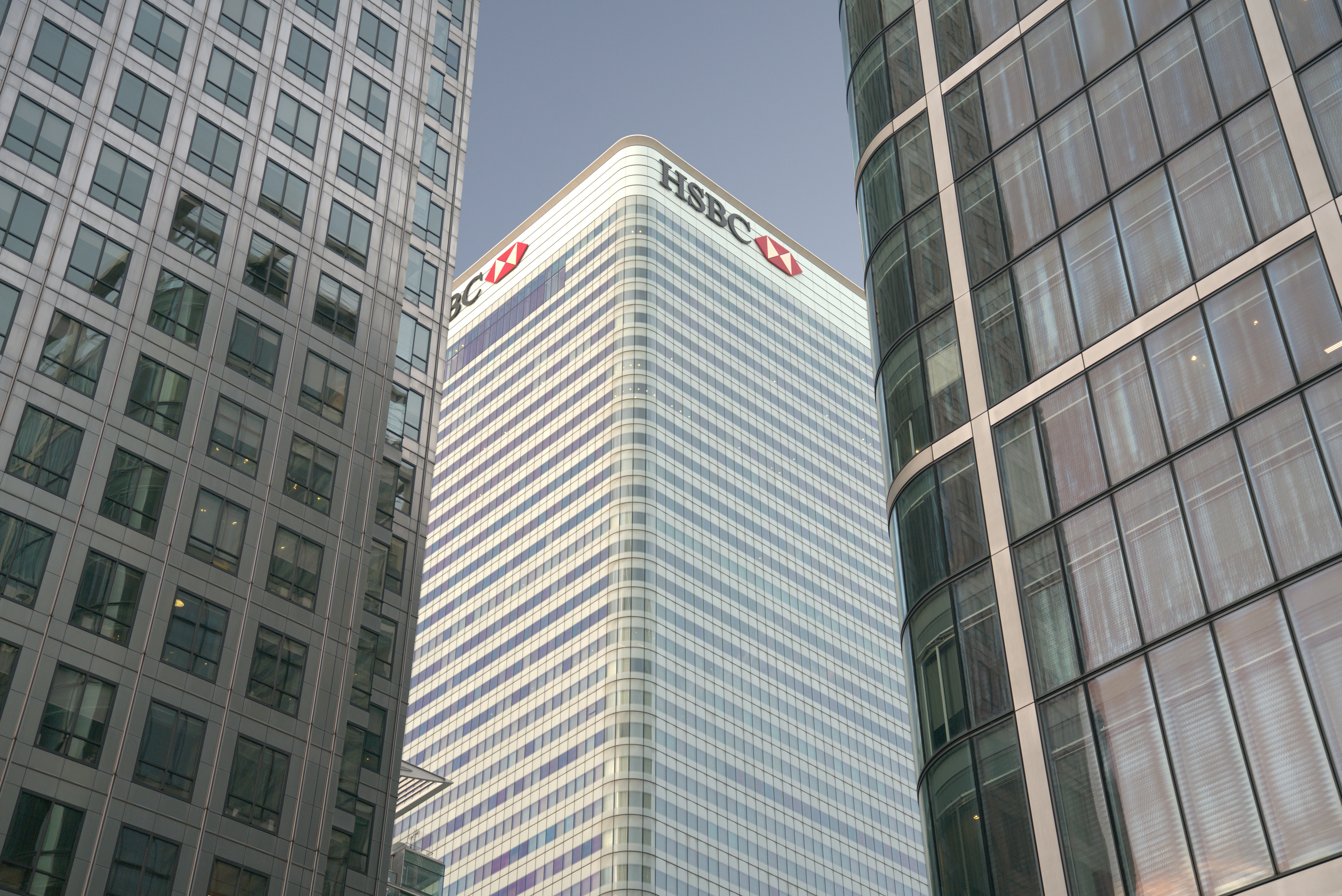 Three modern office towers rise between two glassy façades, with the central HSBC-branded building catching the light and forming a geometric skyline.