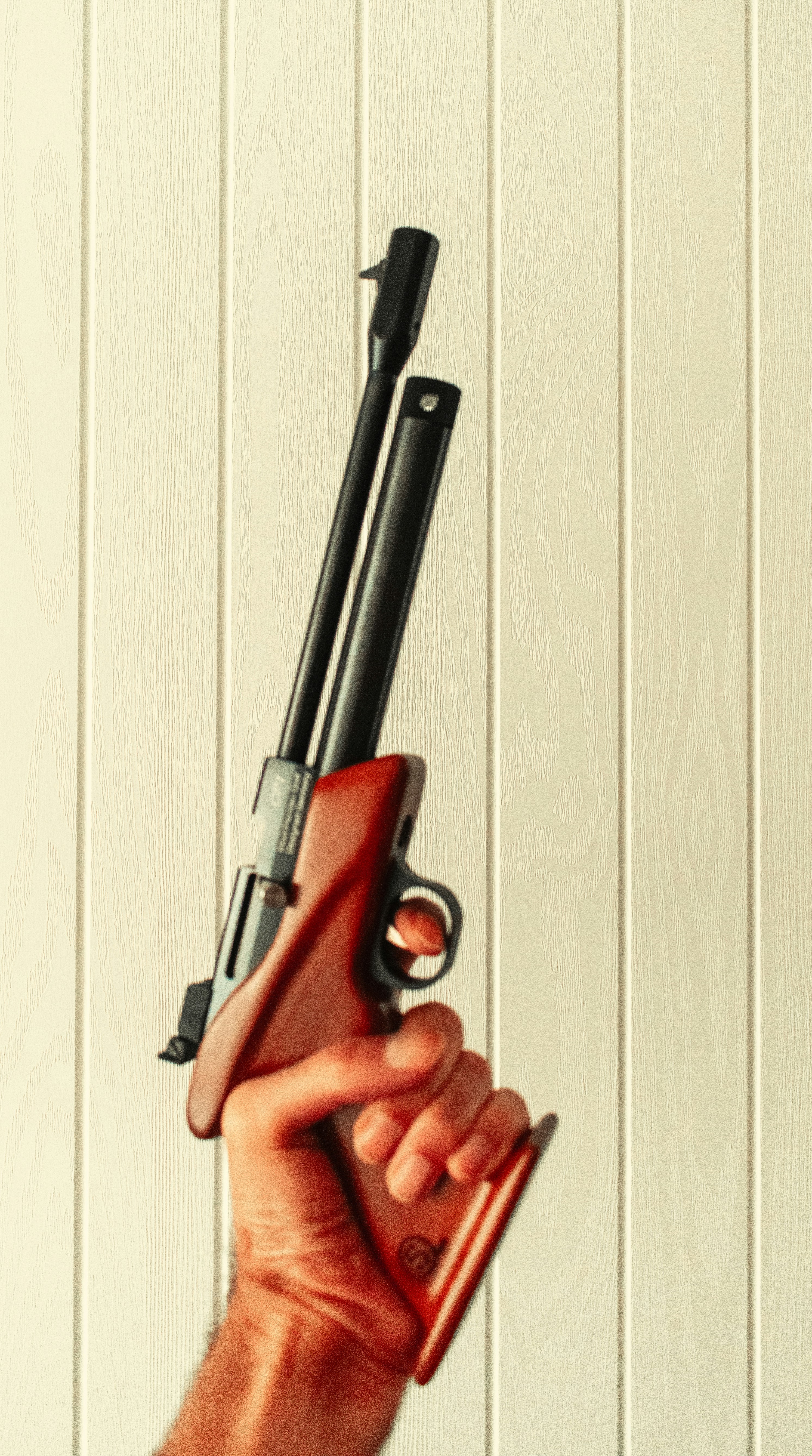 Hand gripping a classic air pistol with a wooden handle.