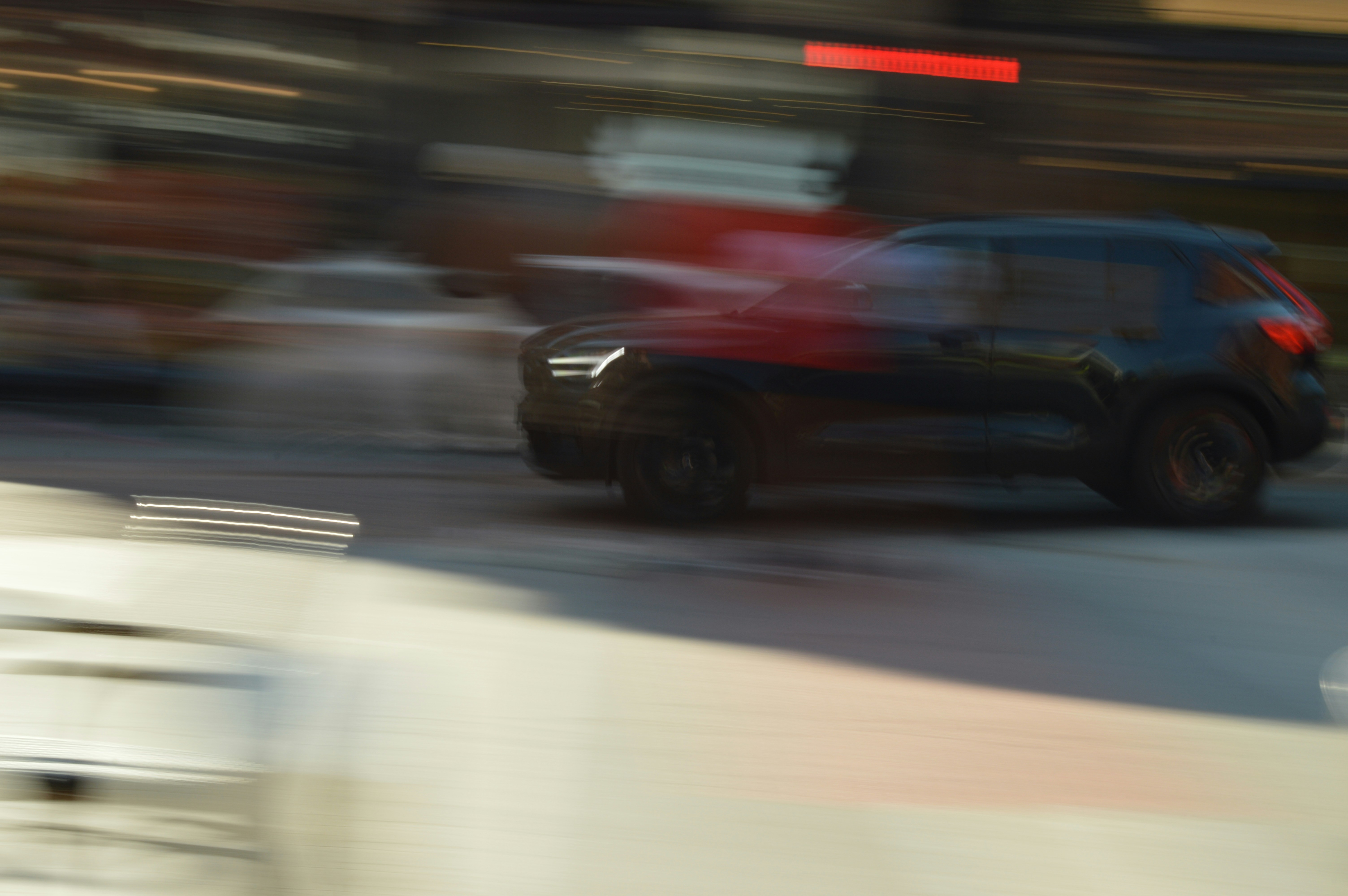 A fast-moving black SUV glides through an urban night scene, creating motion blur across the frame with glowing tail lights and reflected street lighting.