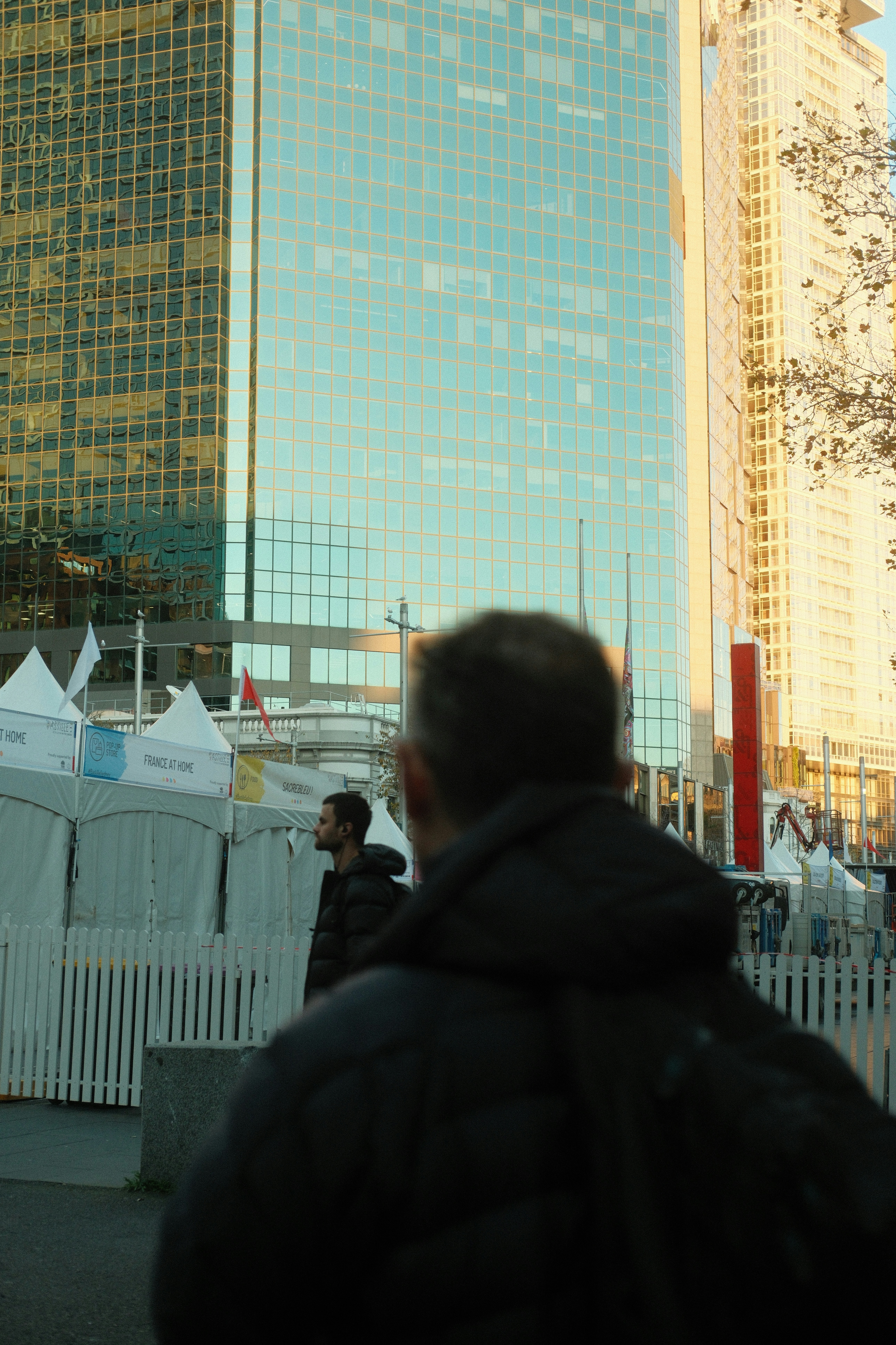 Cityscape Encounter: A Quiet Figure Amid Modern Glass and Tents