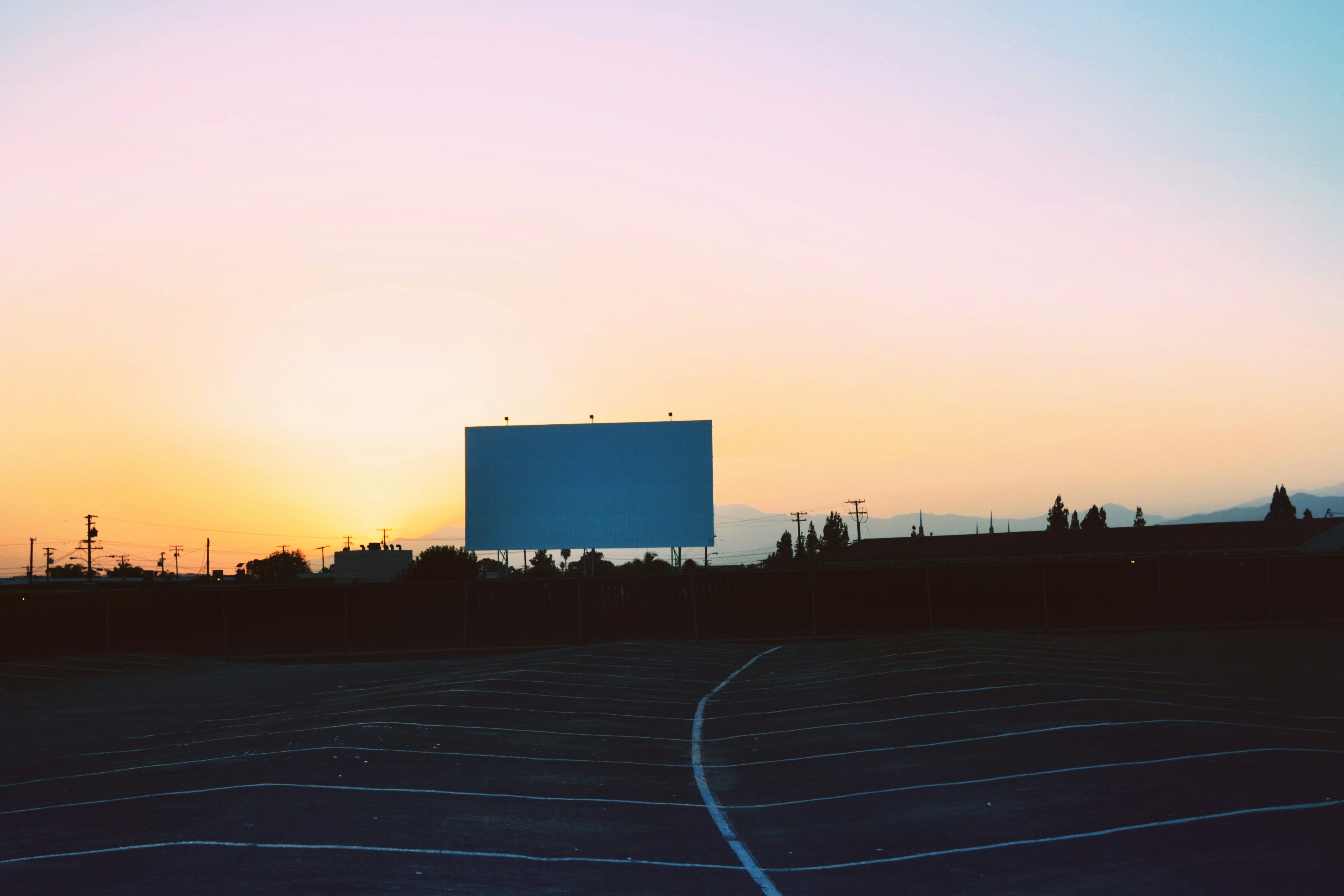 A dormant parking lot at dusk with a blank billboard silhouette against a gradient sky; the scene emphasizes quiet space and a lone, inanimate screen as the focal anchor.