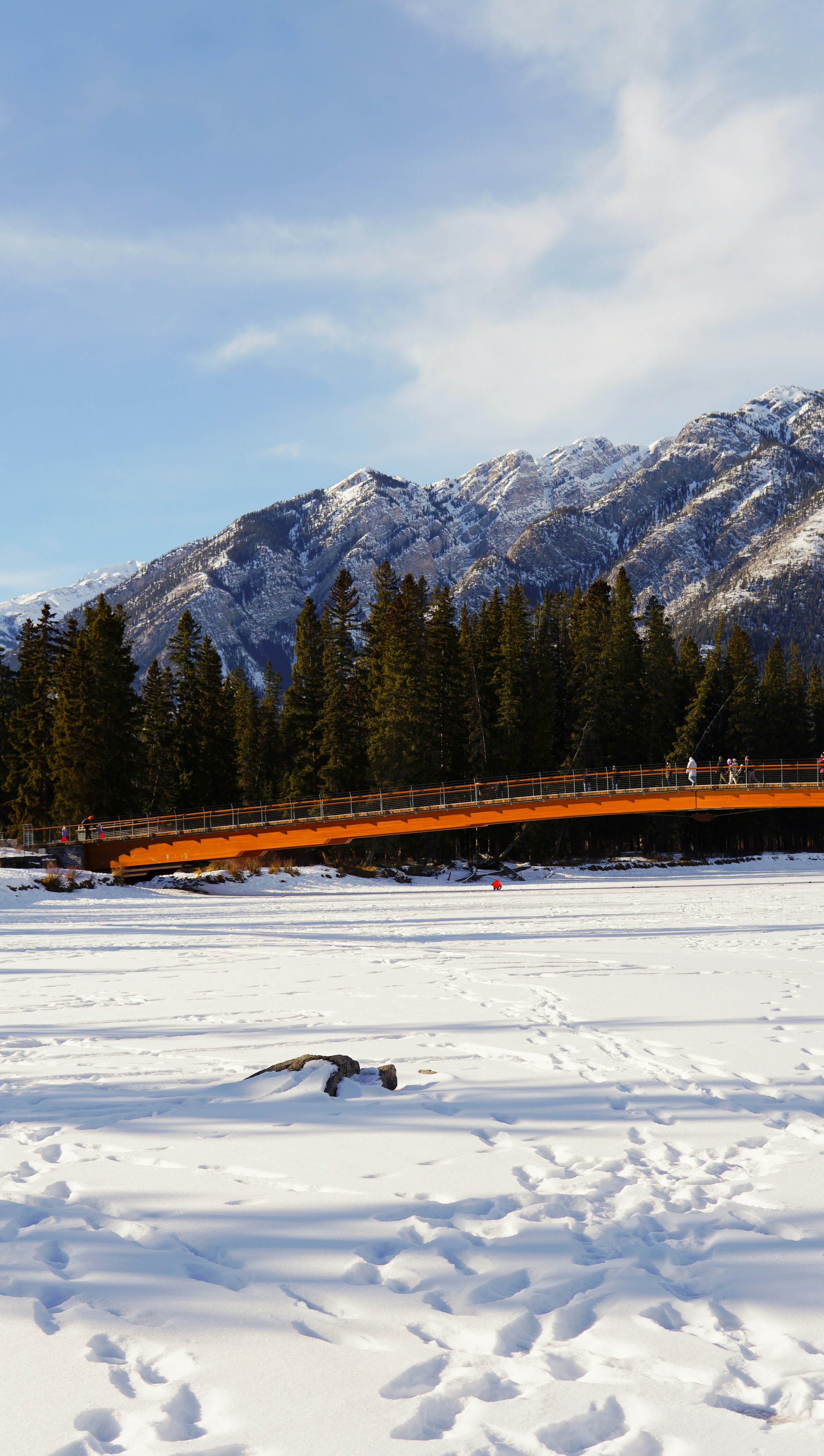 Snowfield Crossing: Orange Bridge Above a Frosted River Under Alpine Peaks