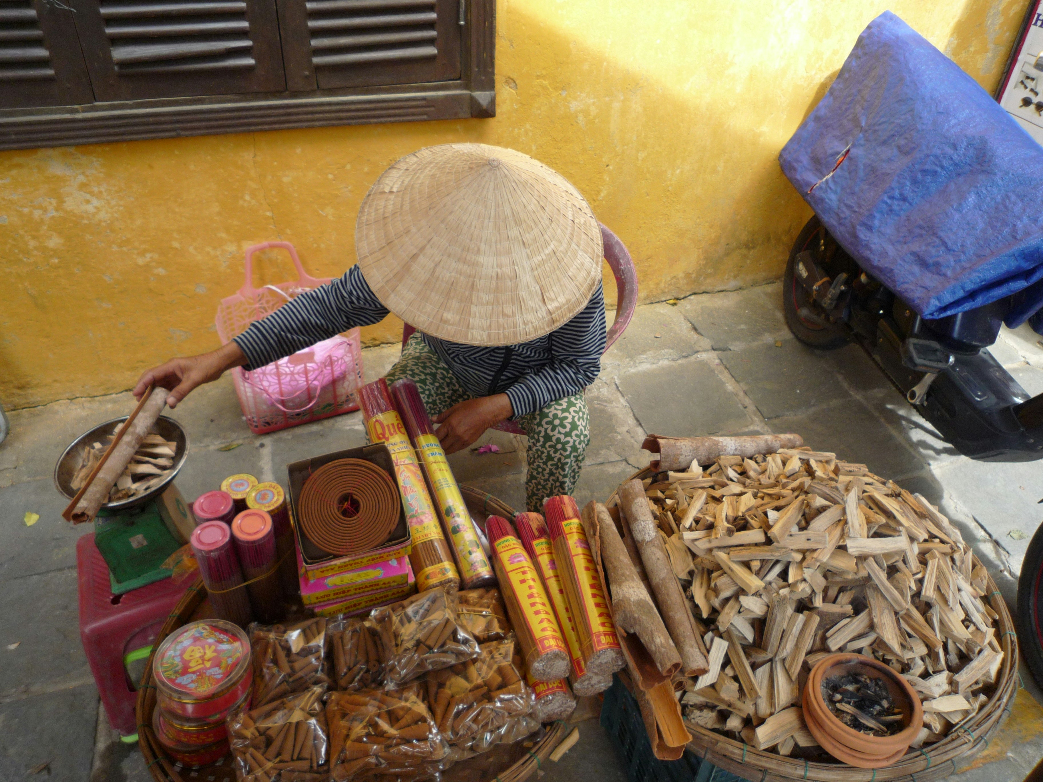 Market Vendor in Traditional Conical Hat Sorting Wood Chips and Spices