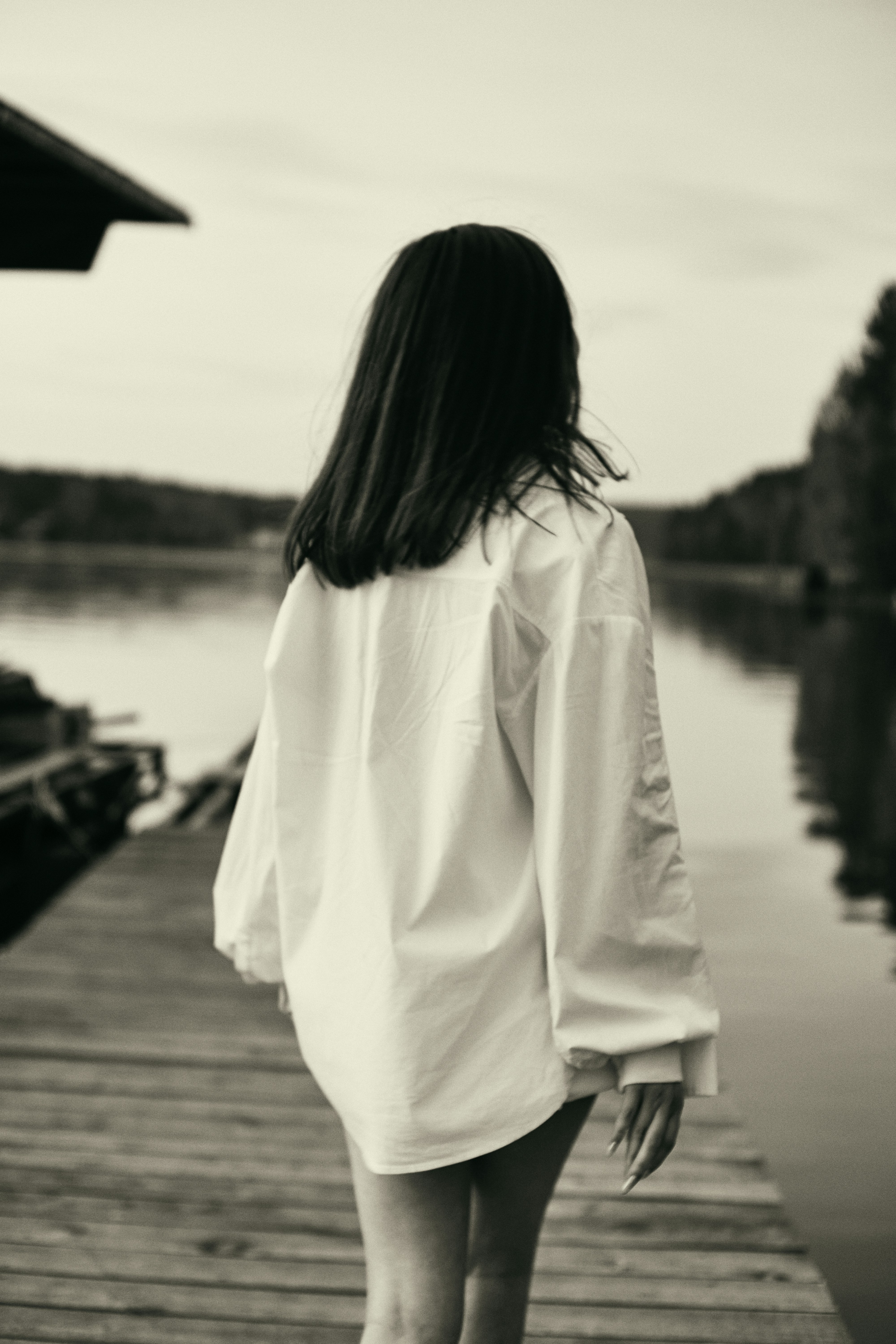 Woman in white shirt walks on dock by a lake.