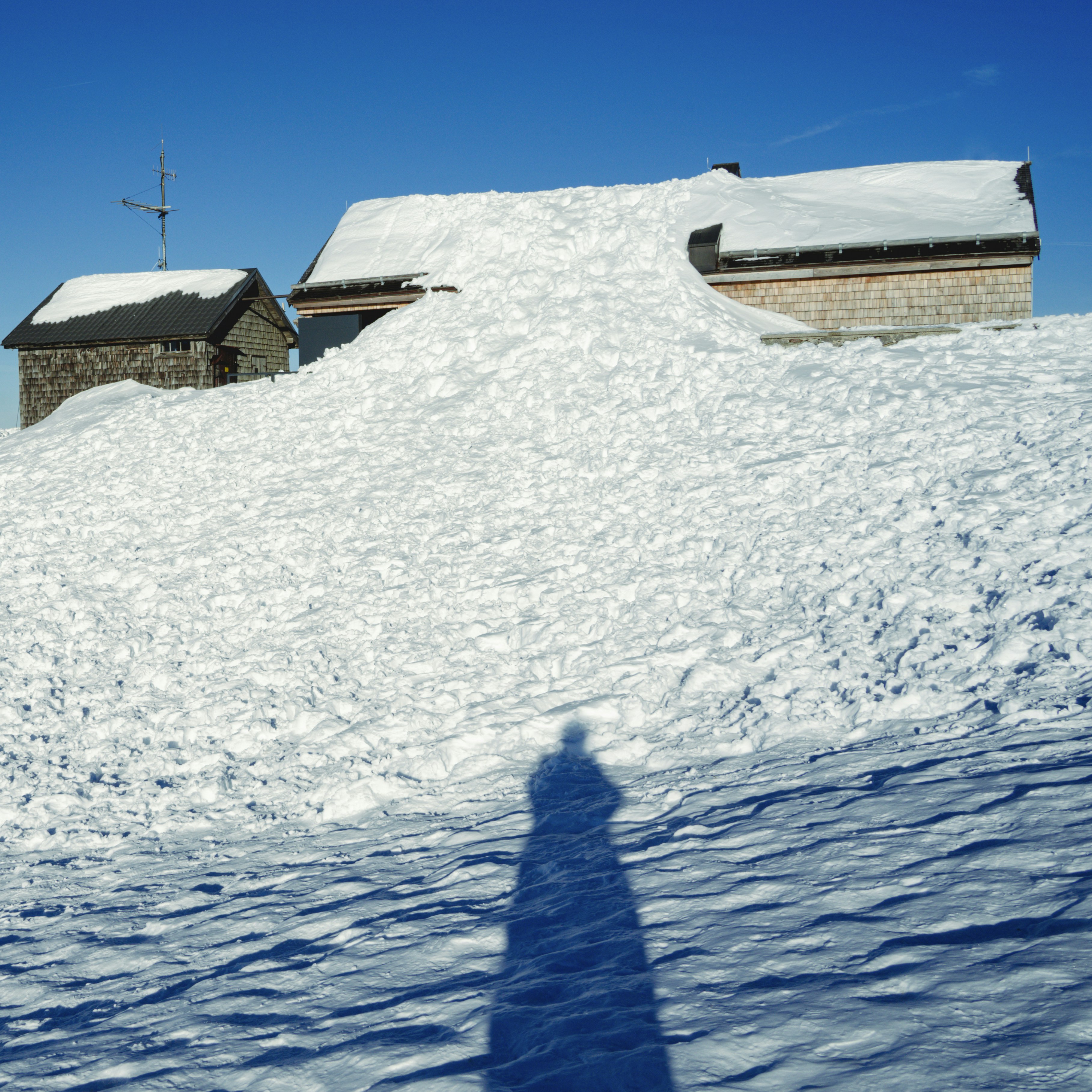 Shadow on the雪: A lone silhouette stretches over a sunlit slope toward the wooden buildings