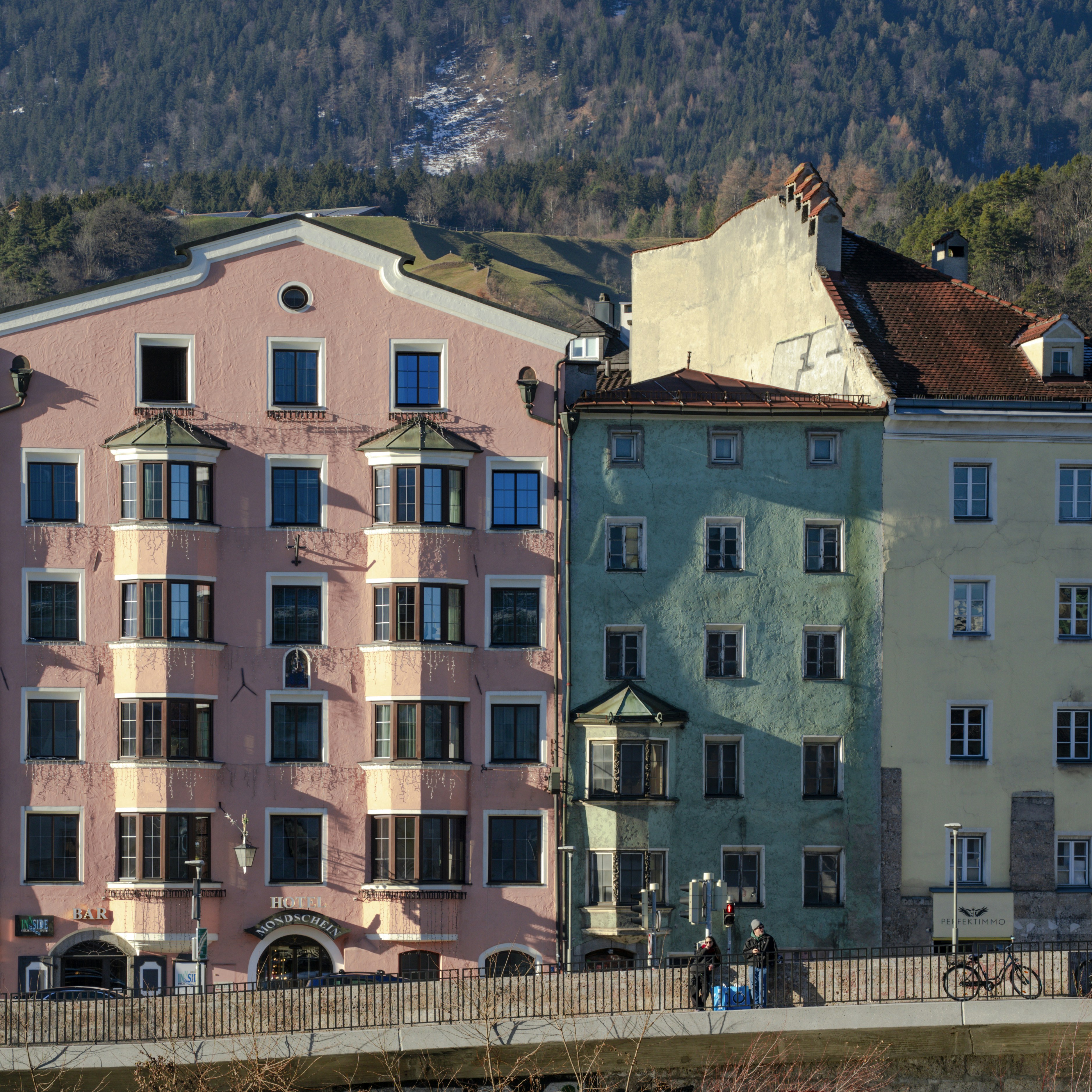 Row of vibrant buildings against a forested mountain backdrop.