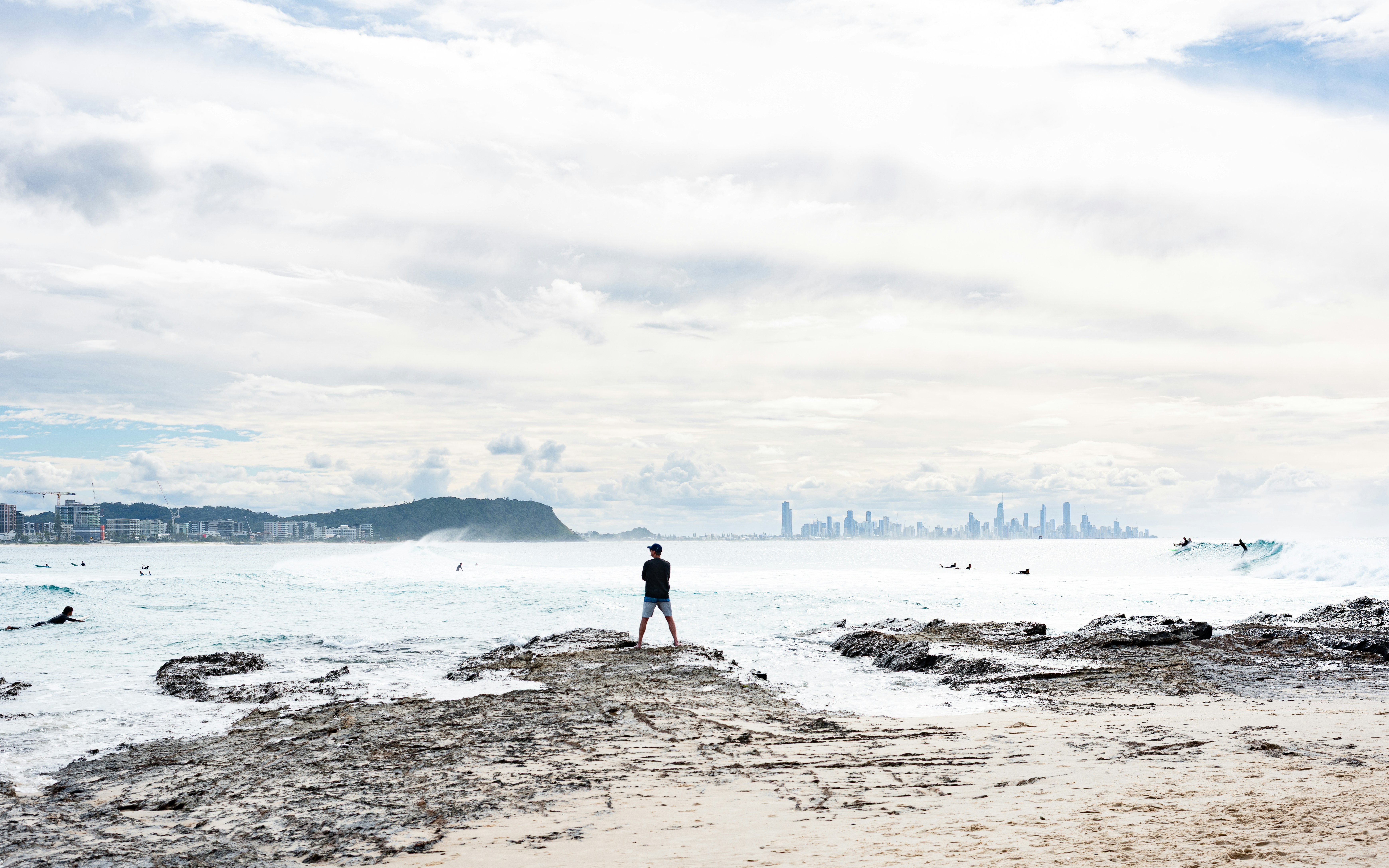 Midday Silhouette: A lone figure anchors the tidal rock at the edge of the sea