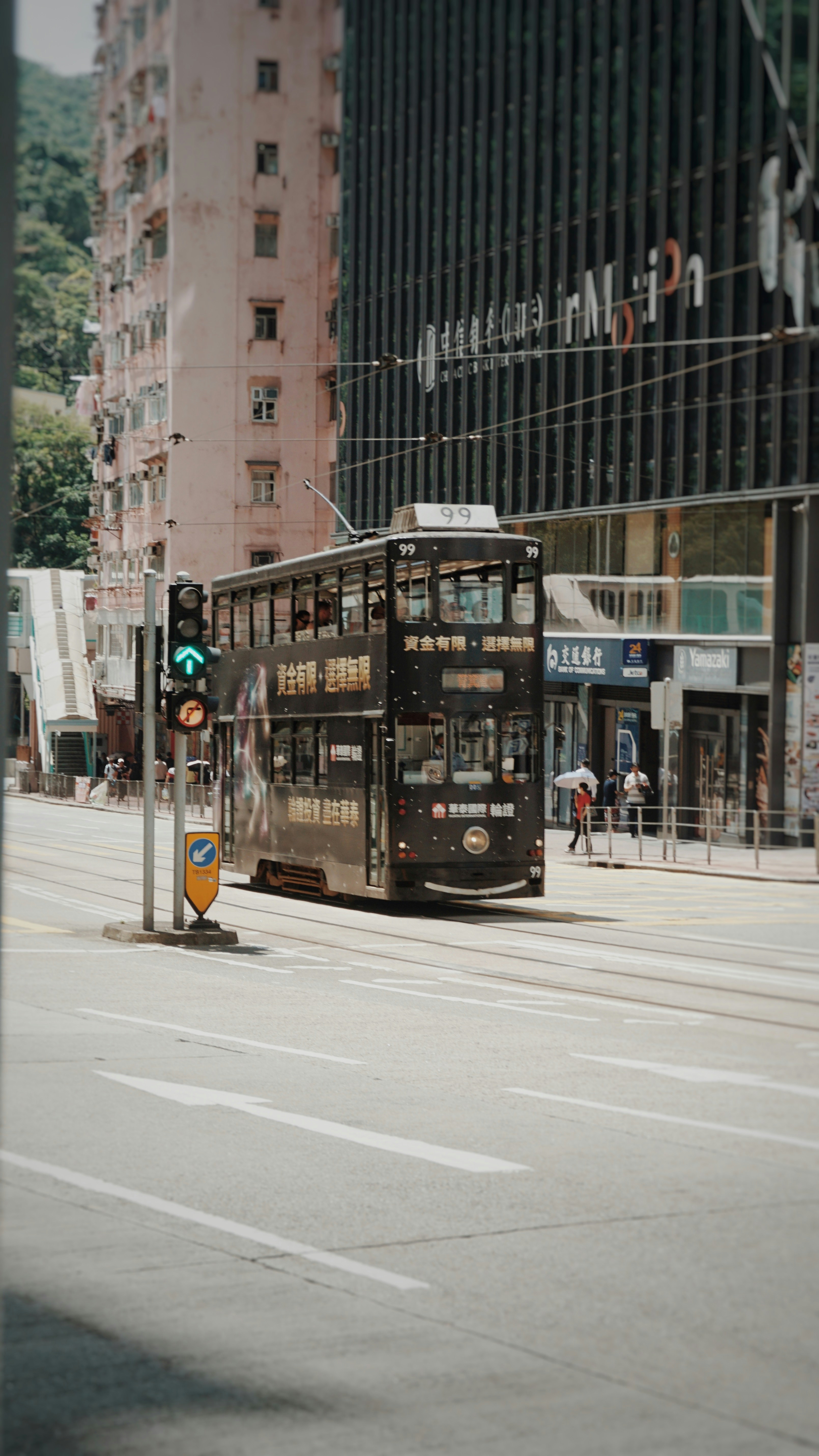 Black tram glides along rails past a busy urban backdrop with tall buildings and pedestrians, capturing a moment of everyday transit in a dense cityscape.