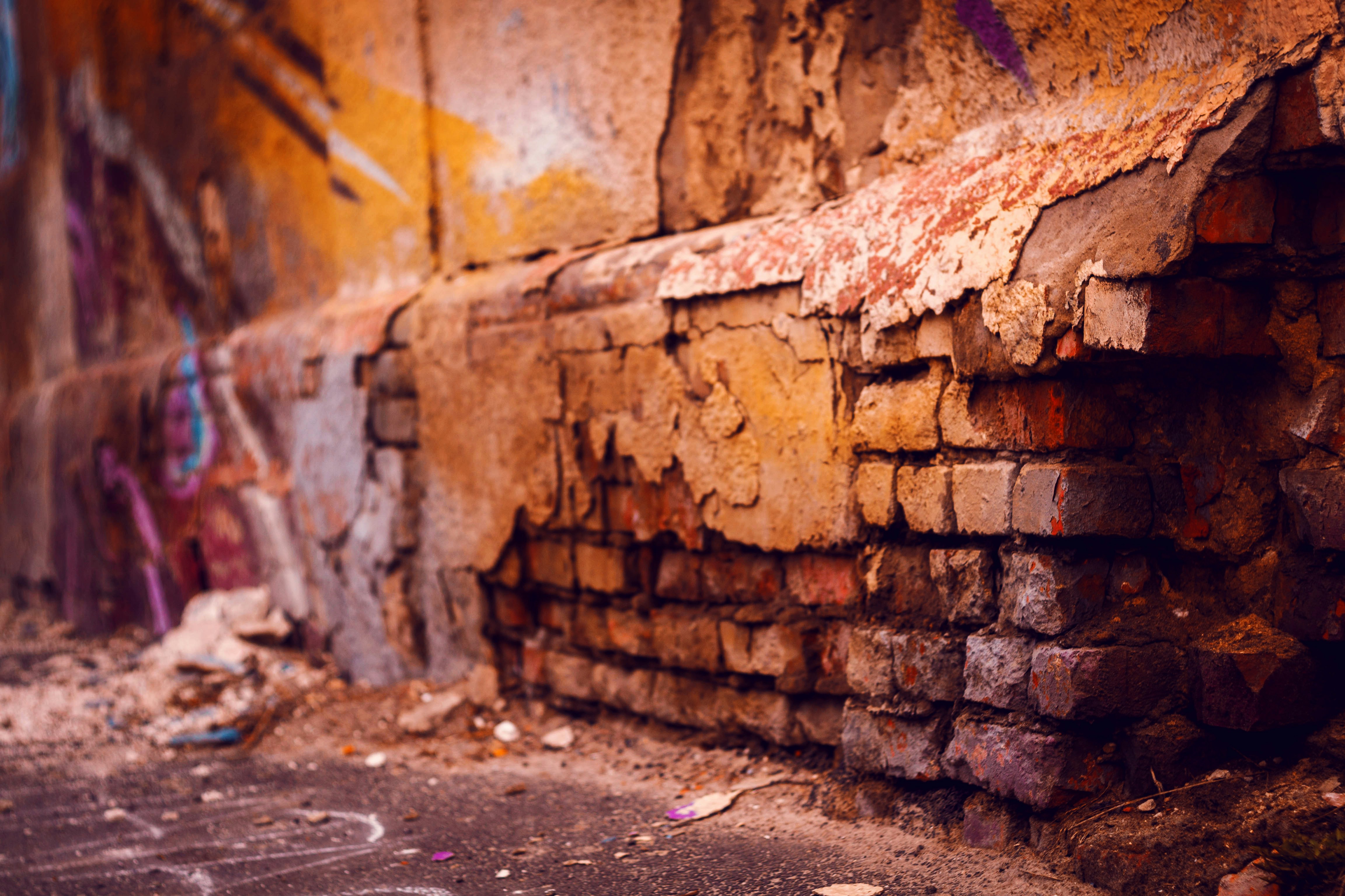 Crumbled brick wall with weathered graffiti at street level