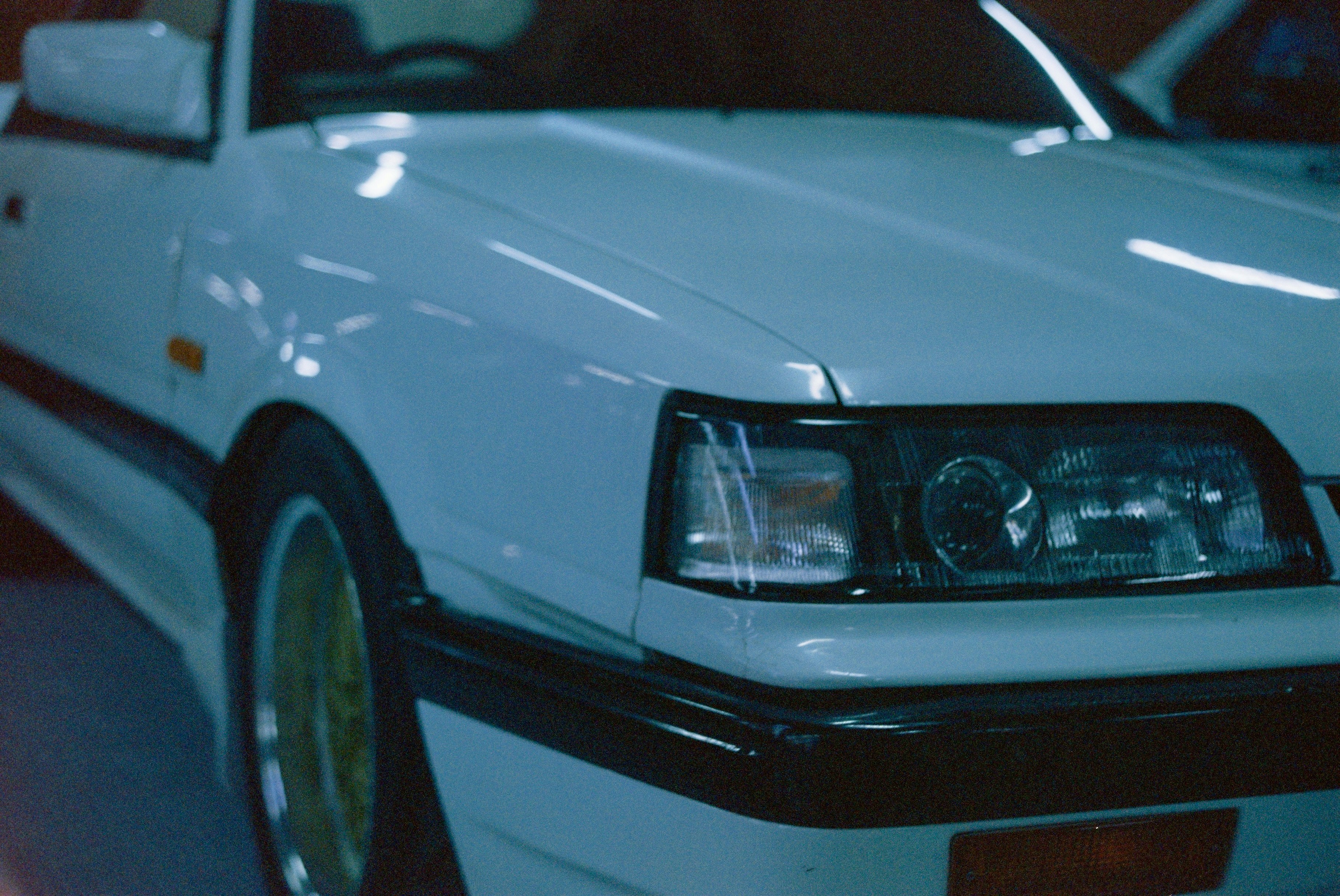 White sedan’s front half under soft showroom glow