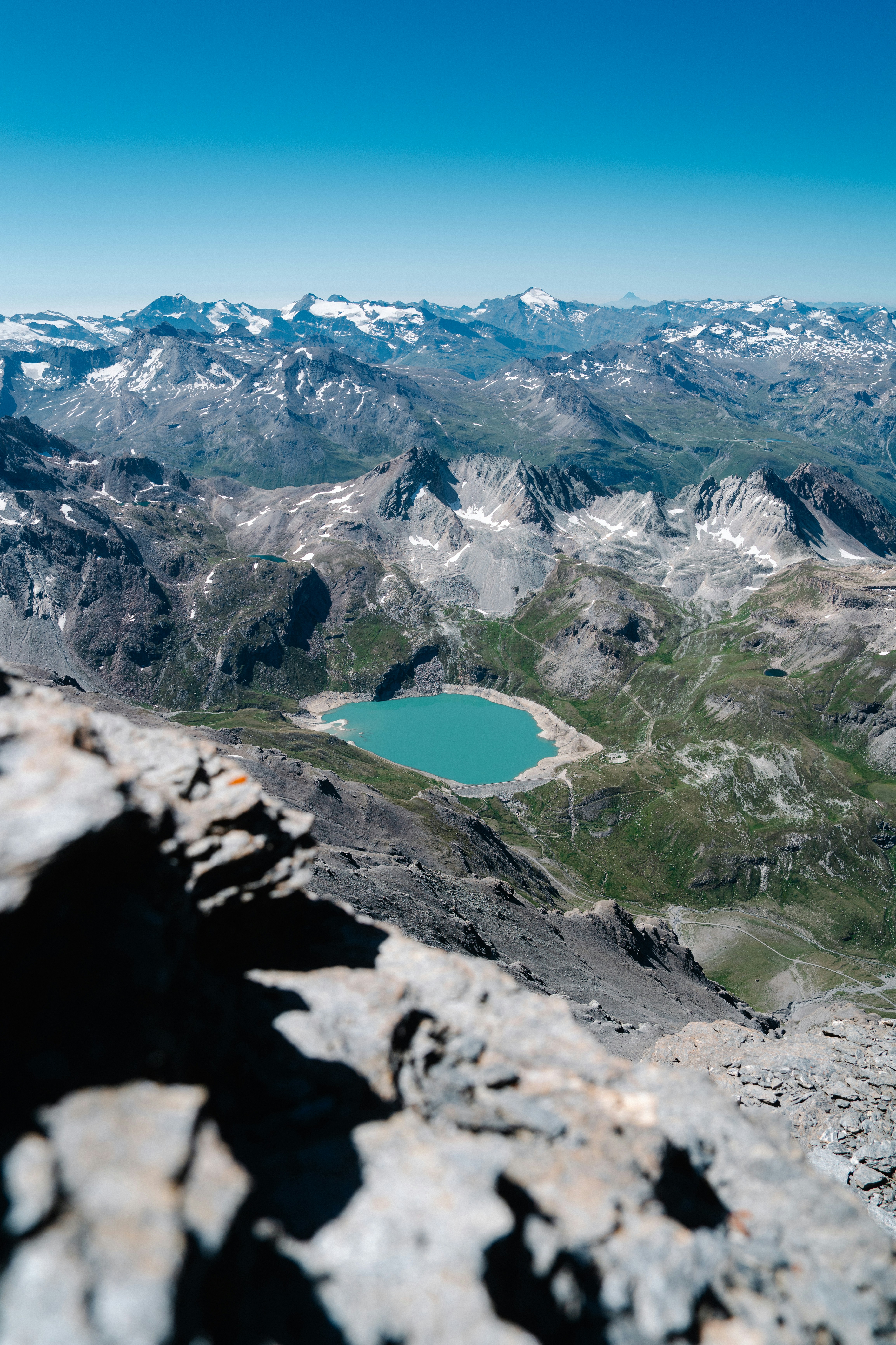A turquoise crater lake rests amid jagged alpine ridges beneath a cerulean sky