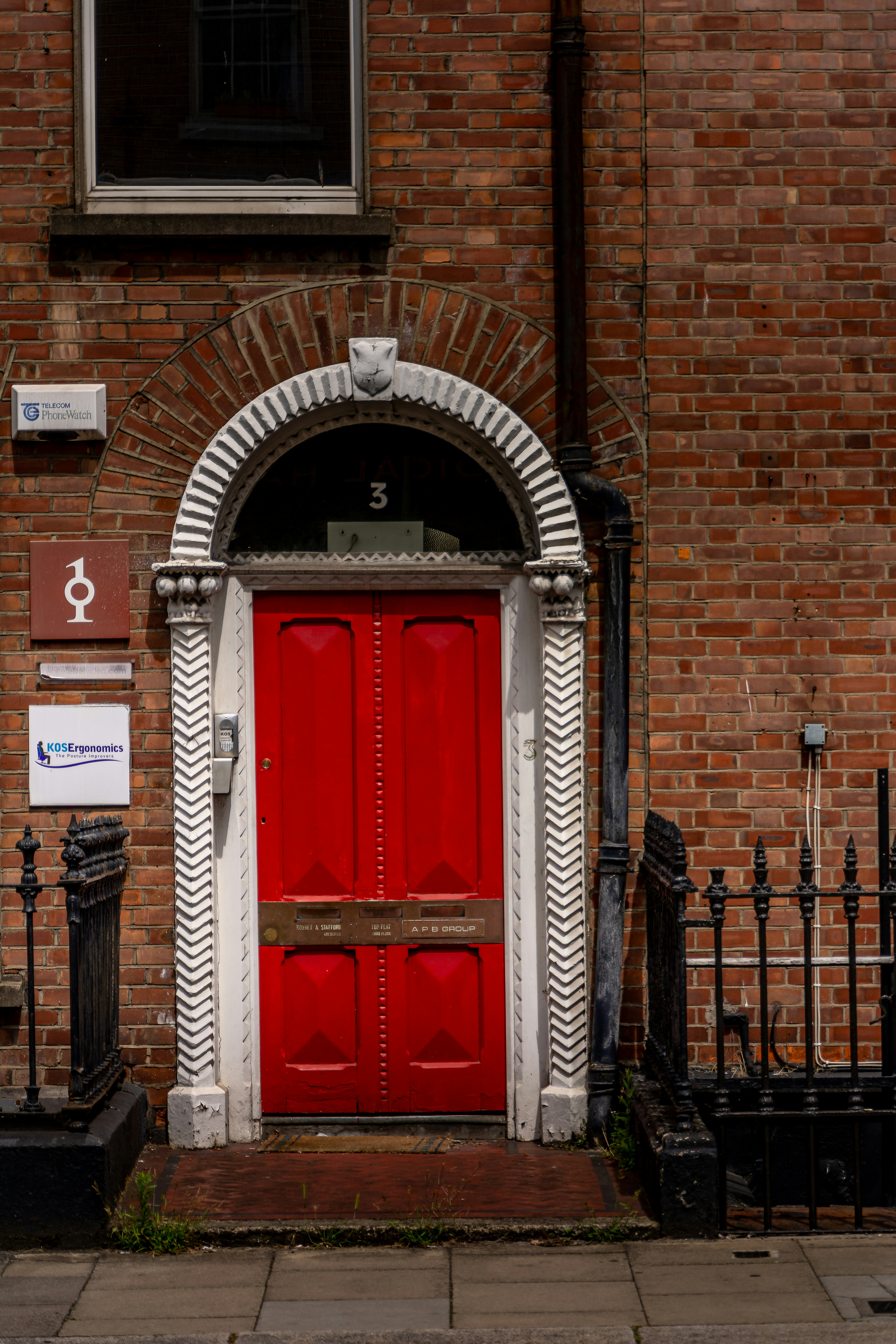 Red Door on a Brick Facade: A City Doorway Framed by Arch and Rail