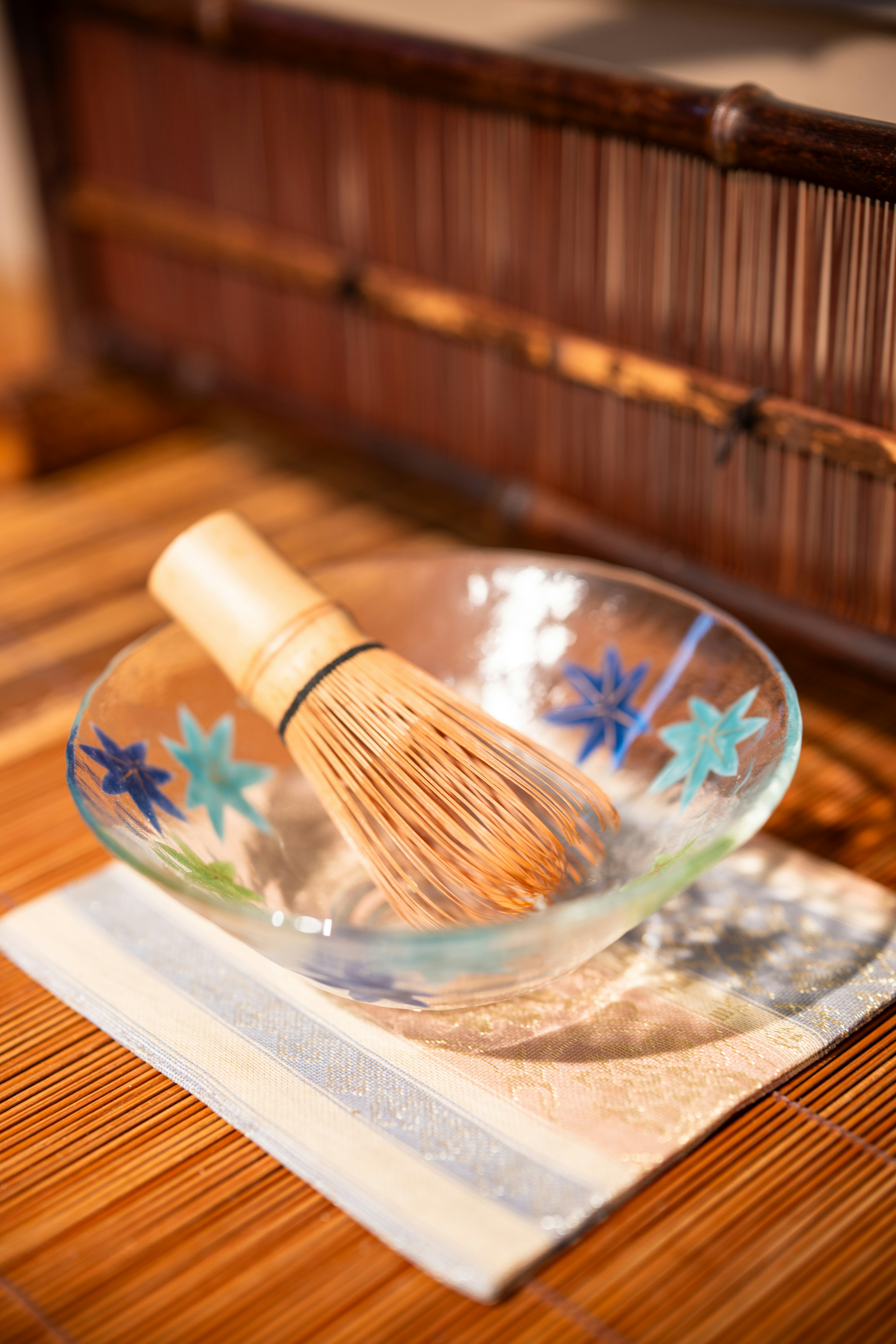Bamboo whisk resting in a glass bowl on a lacquered wooden surface