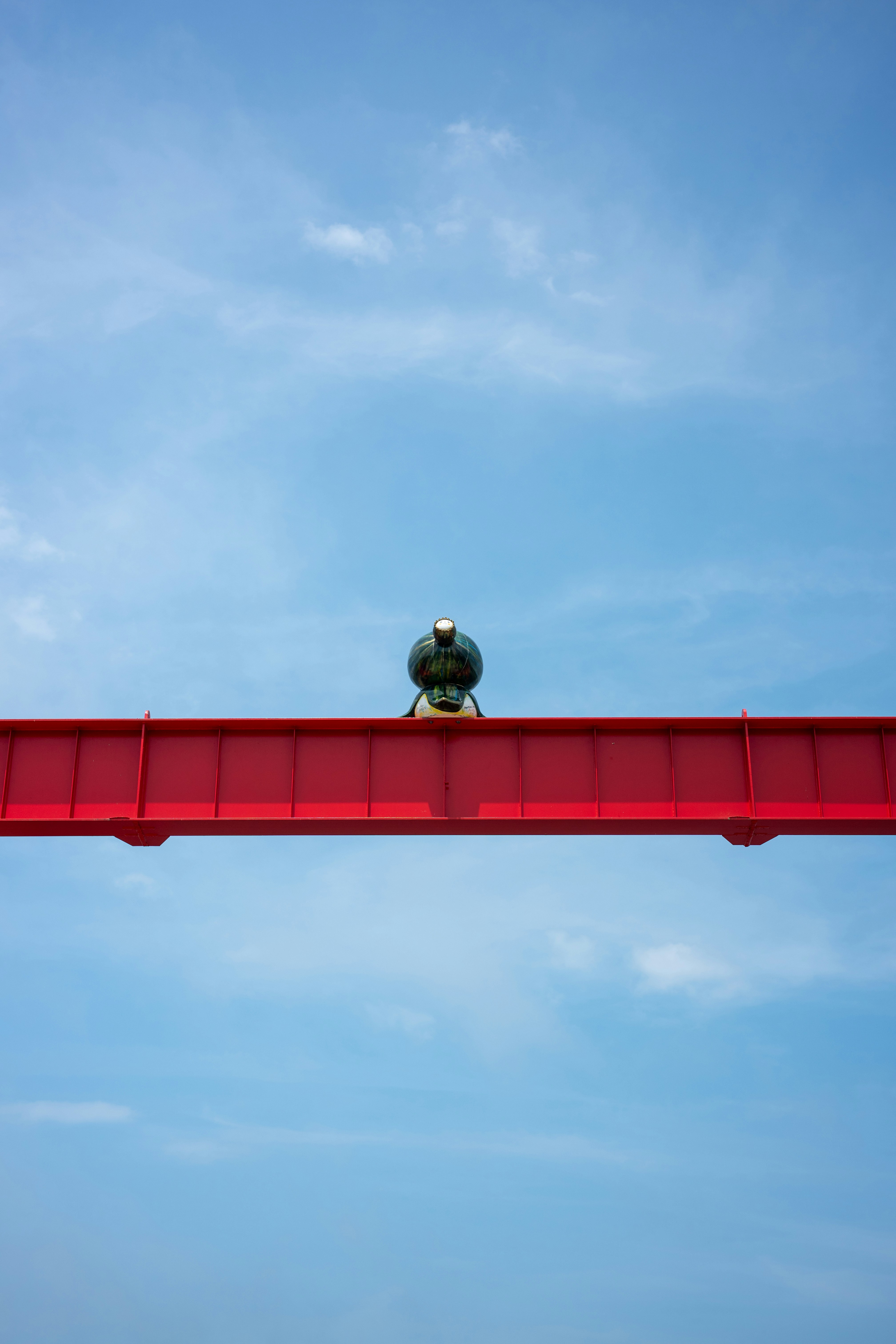 Red Beam Span Suspends a Sole Ornament Against an Aerial Blue