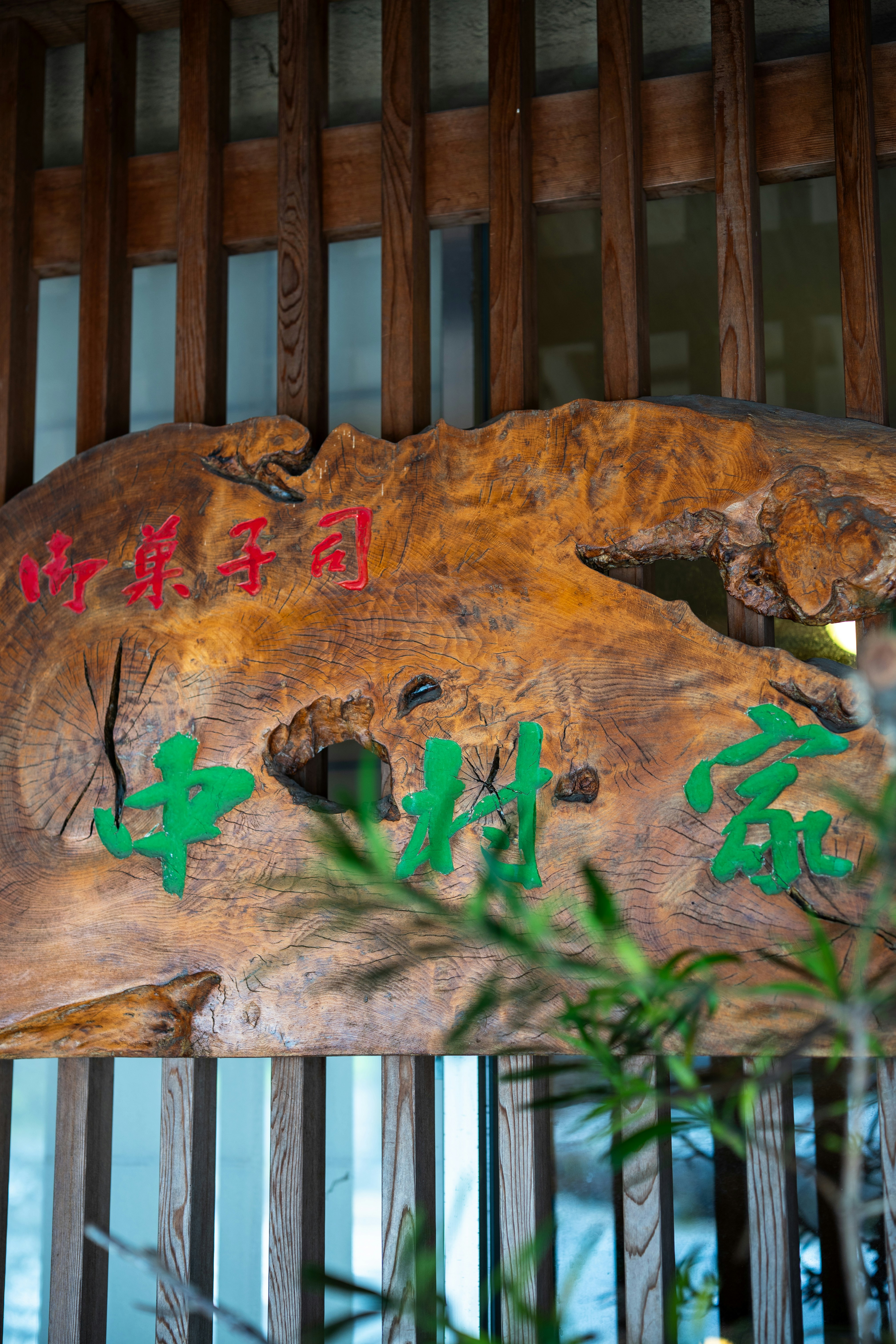 Carved wooden sign with red and green Chinese characters against vertical slats