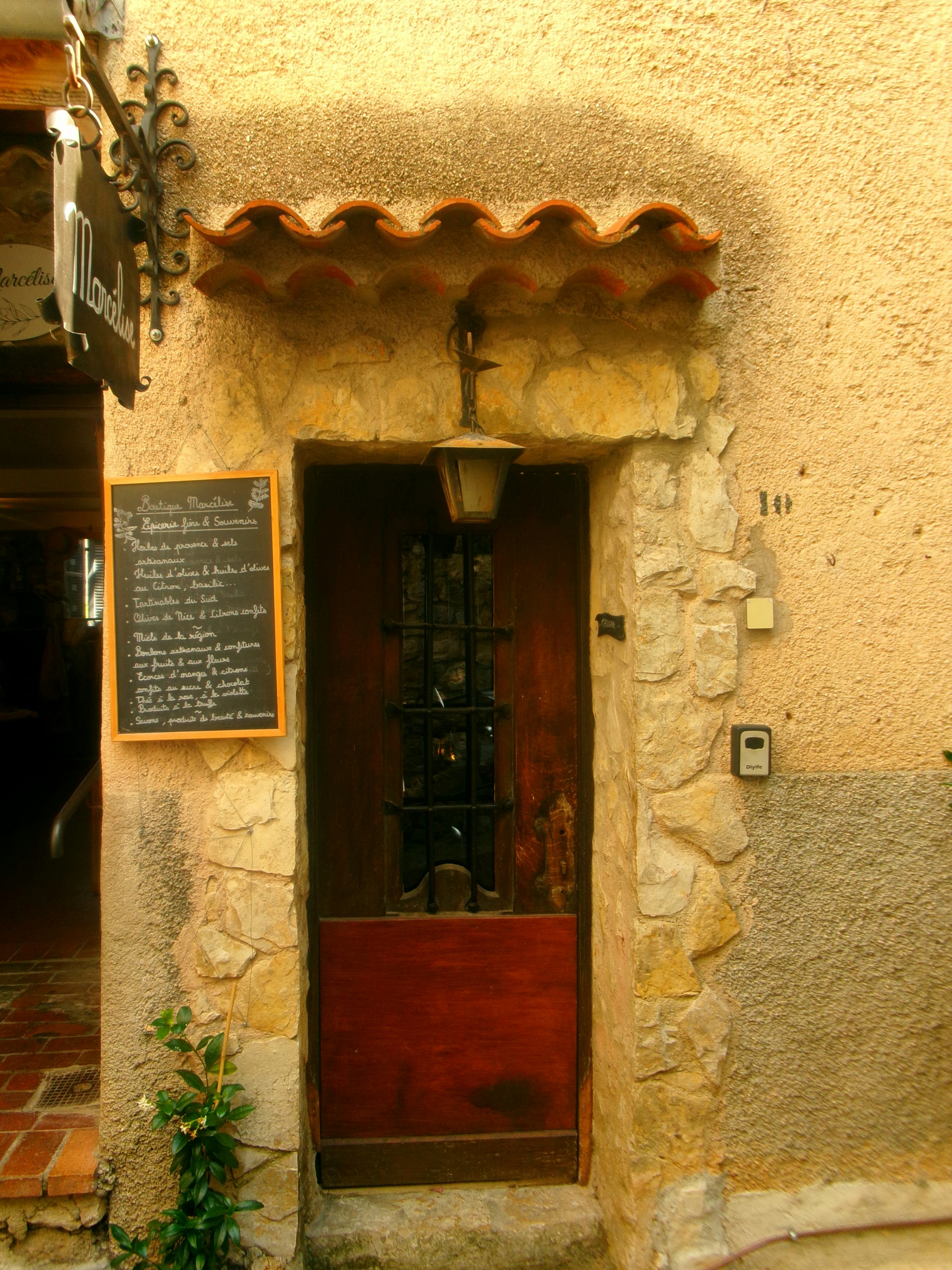 Weathered doorway in sunlit stucco facade with dark wooden door and iron grate