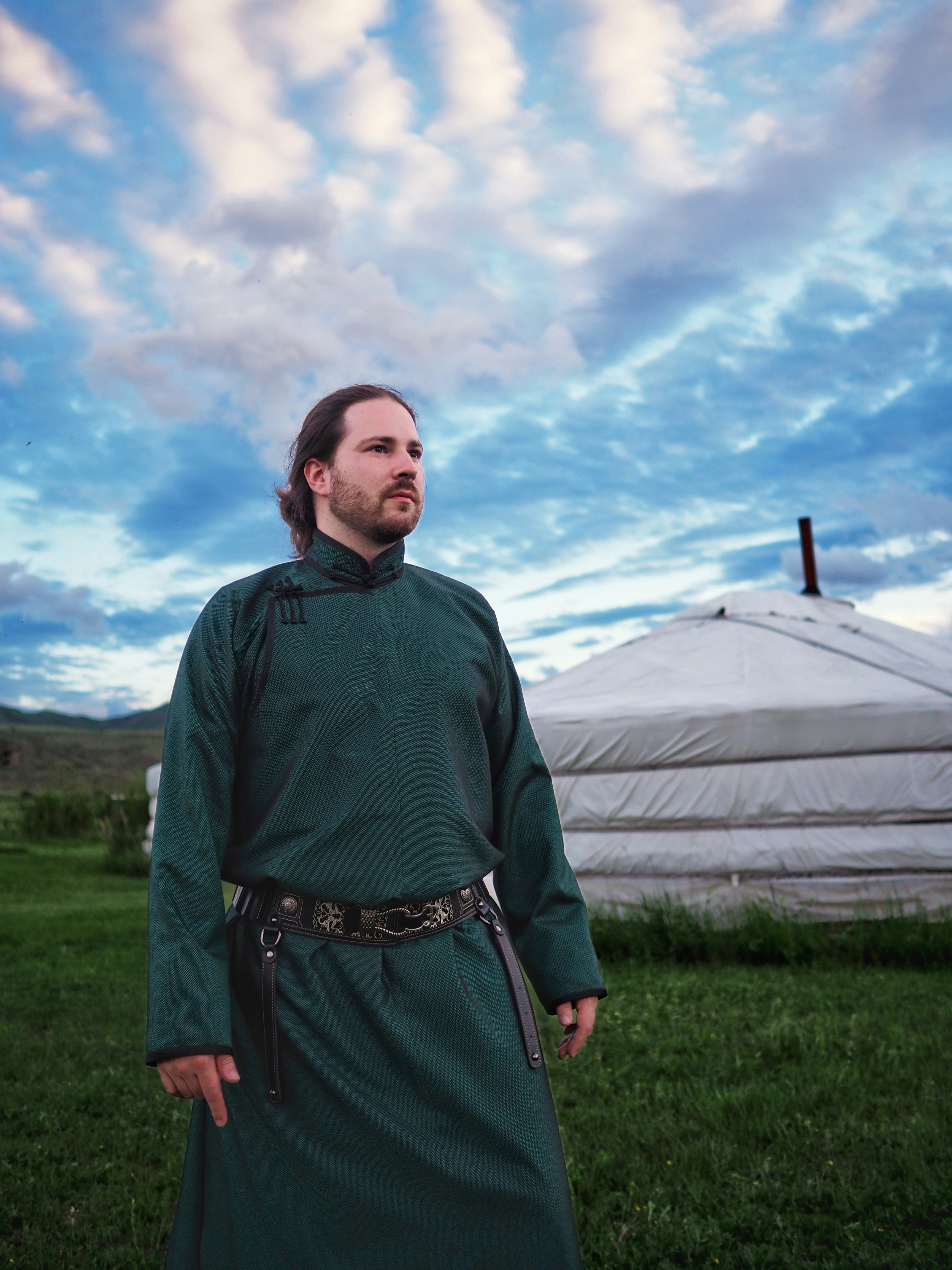 Green-clad wanderer under a vast sky near a white yurt
