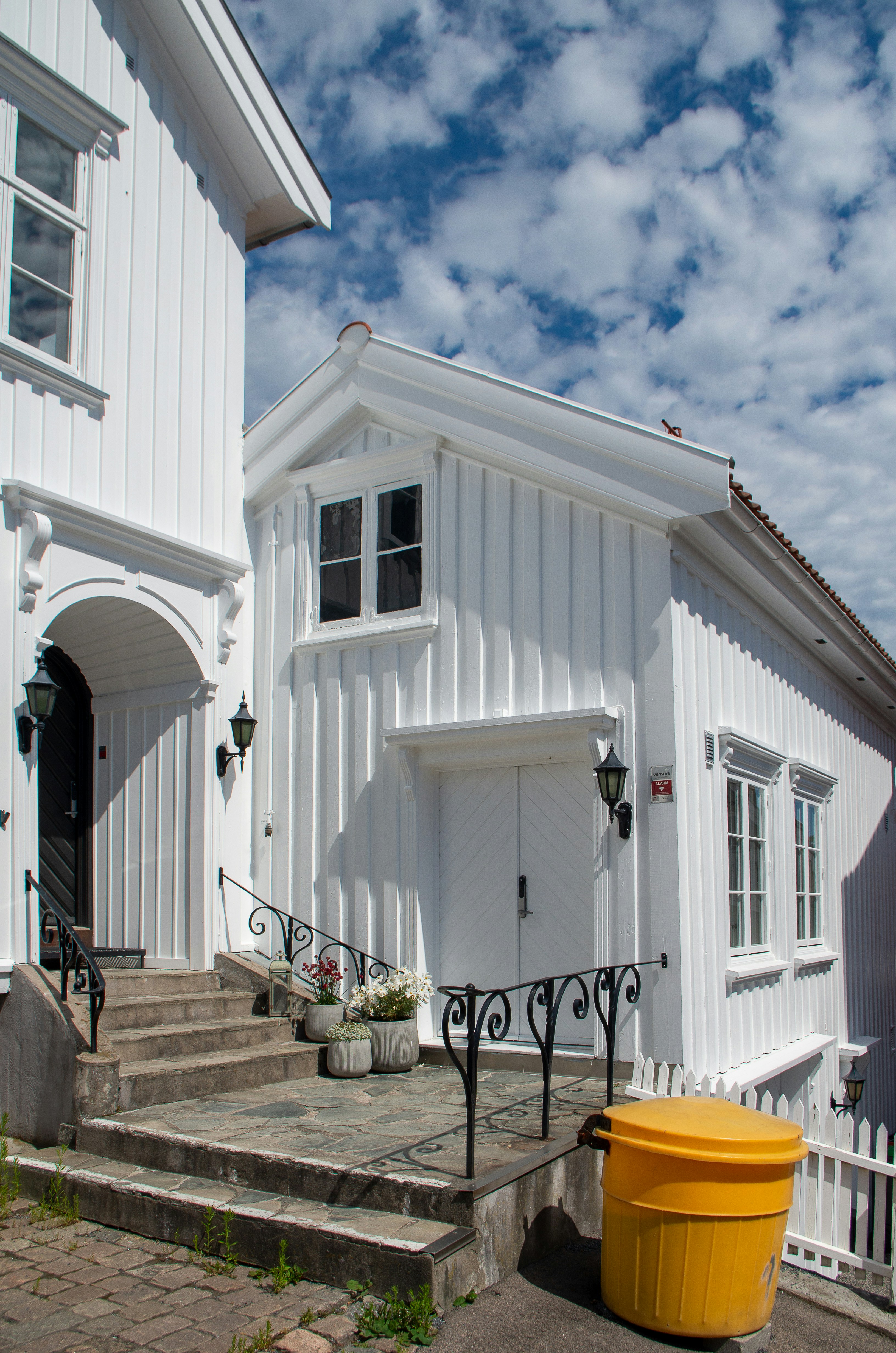 Sunlit white townhouse with curved iron railing and bright yellow bin