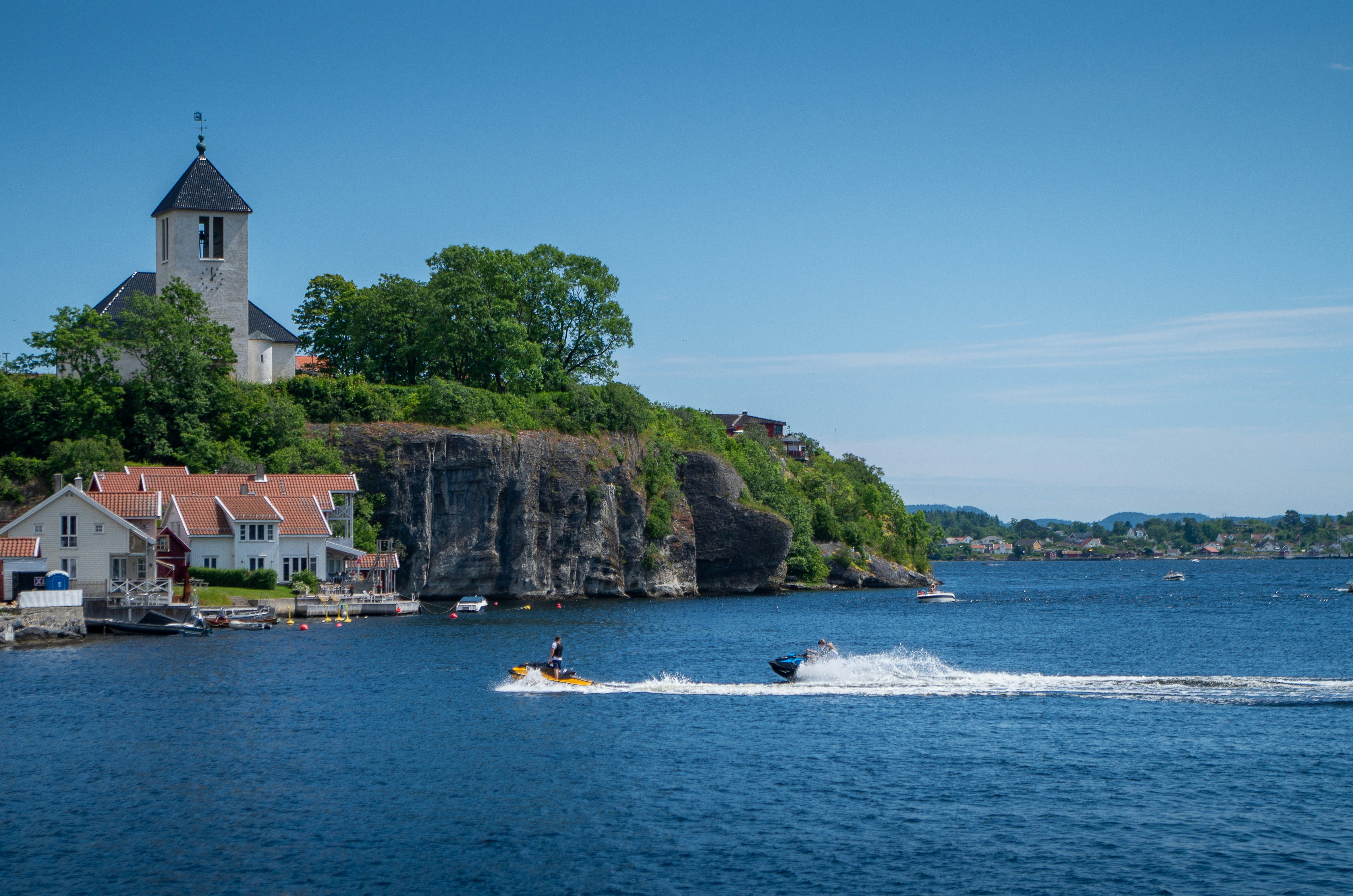 Harbor village with cliffside church and speedboats over blue water